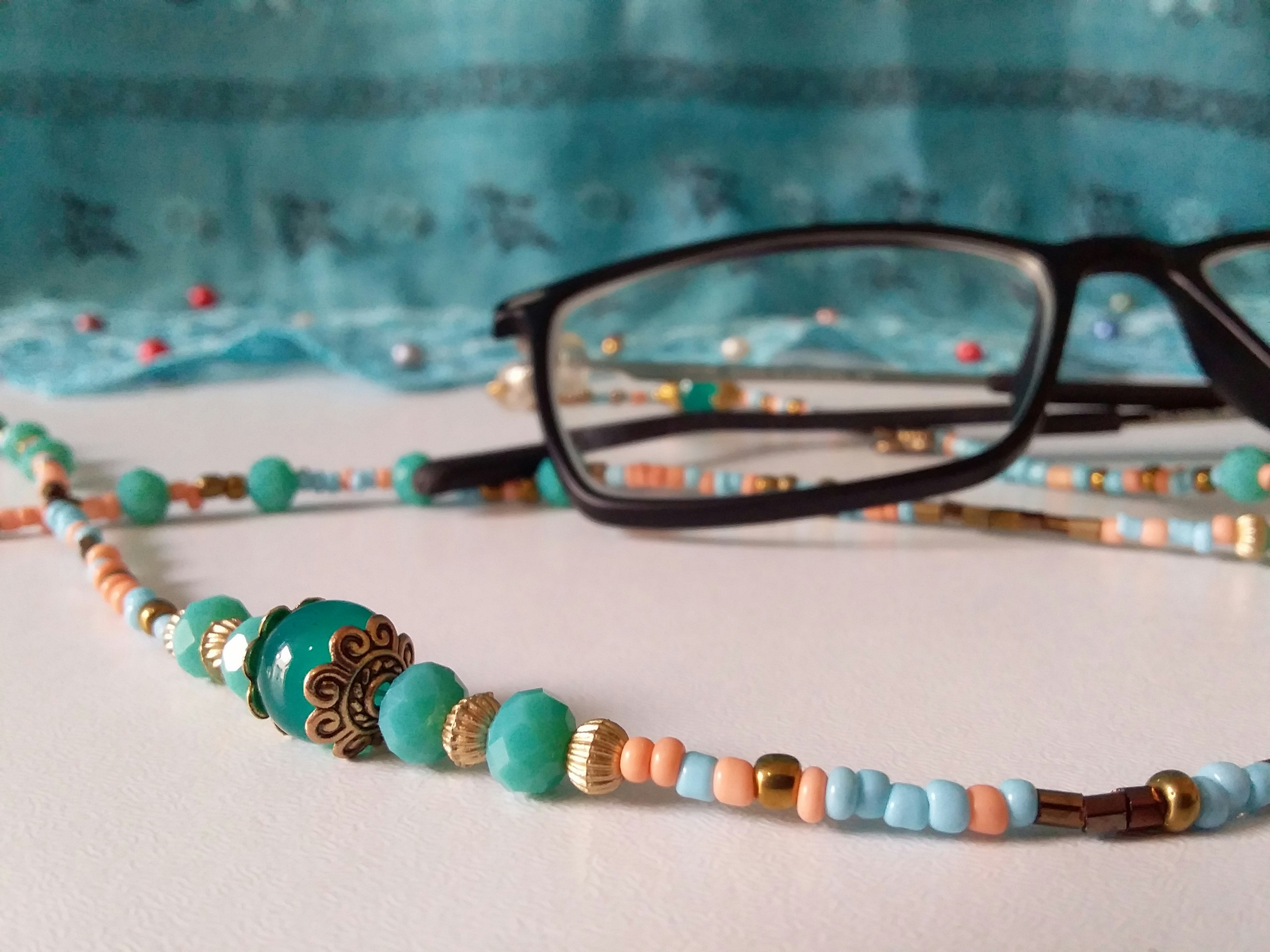 Black-framed eyeglasses rest on a blue fabric adorned with colorful beads.