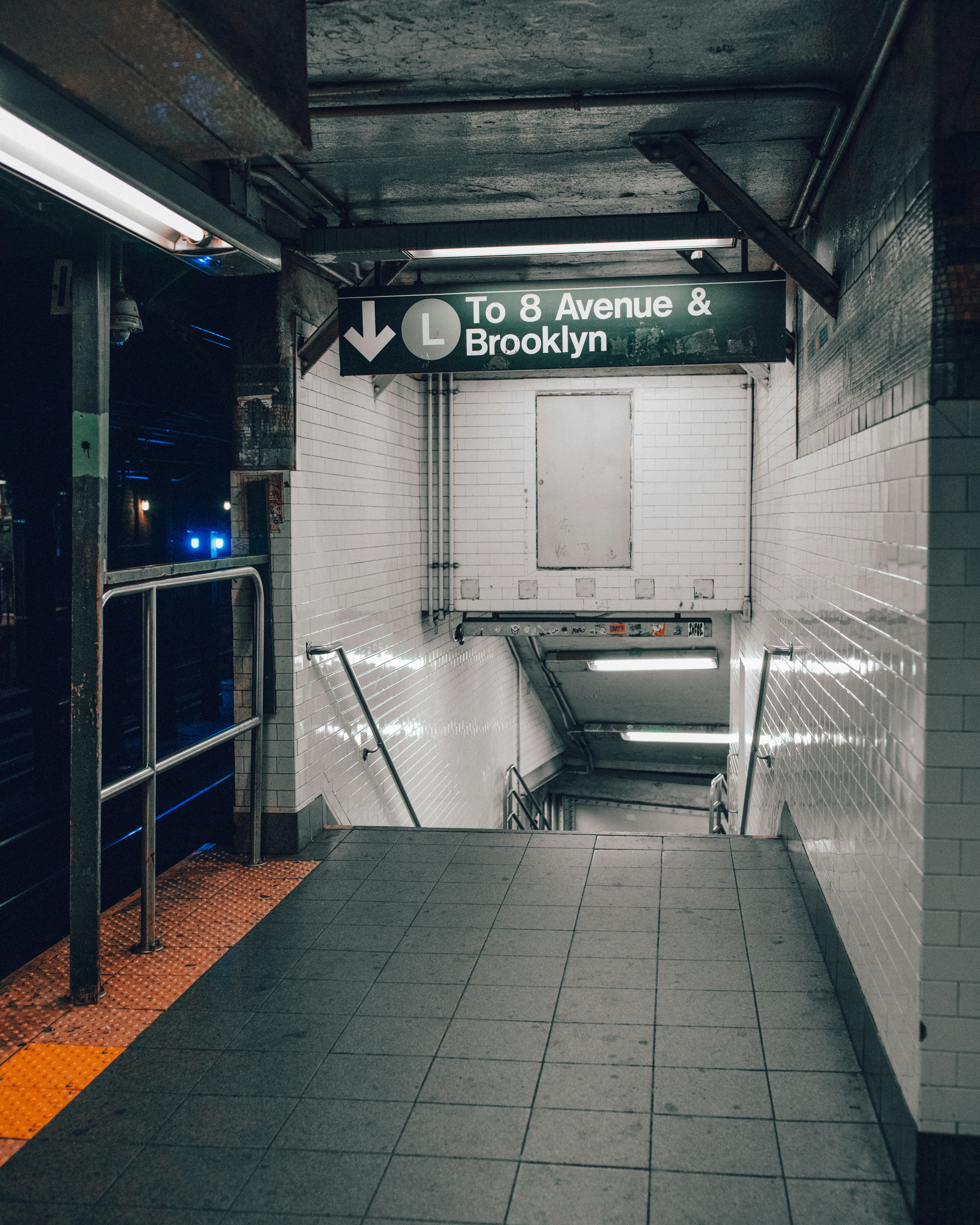 Subway entrance leading to 8 Avenue & Brooklyn, featuring tiled walls and illuminated signage.
