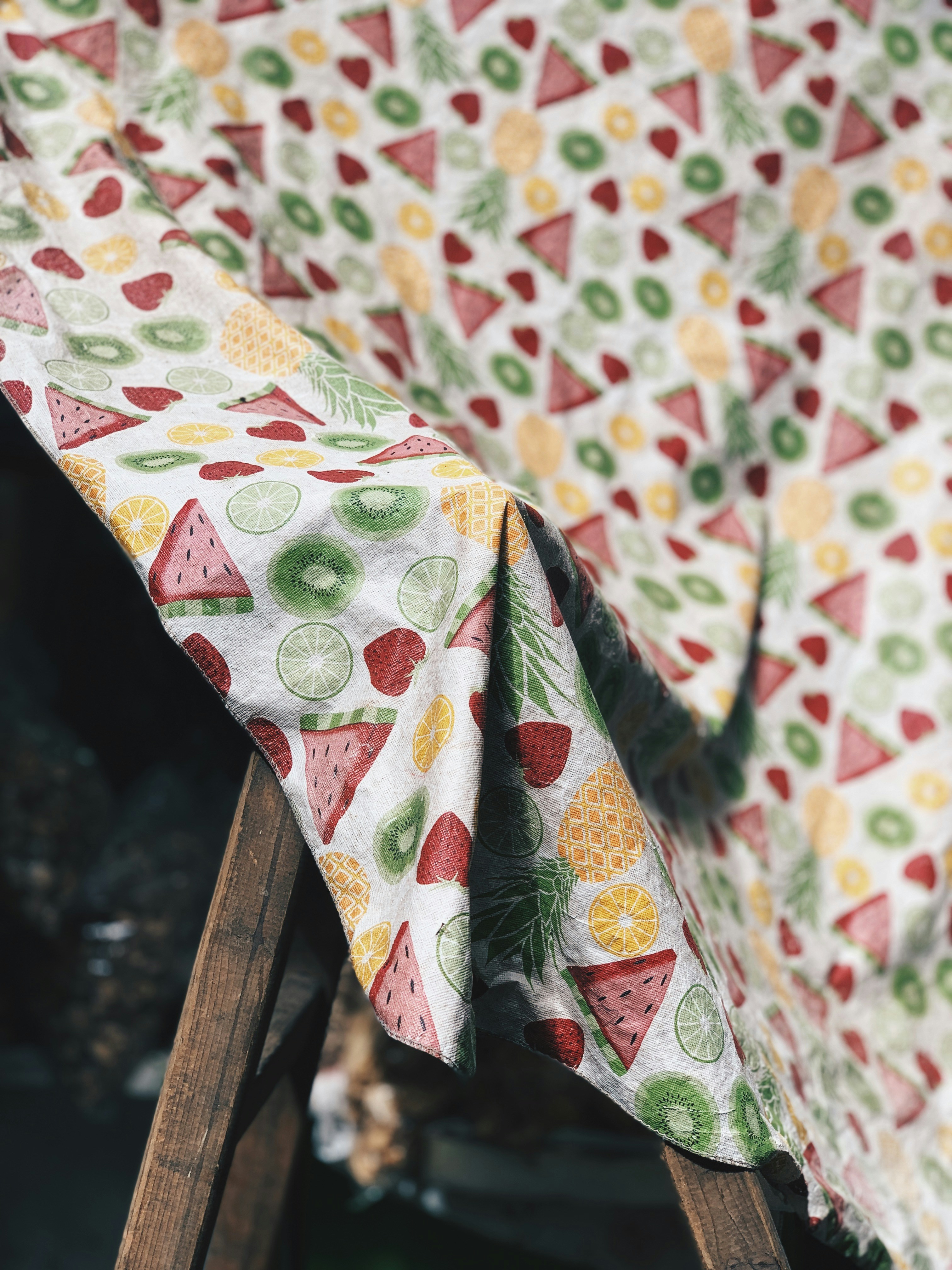 Colorful fruit-patterned fabric drapes over a wooden frame, creating soft folds and a textured background. The scene emphasizes the fabric texture and print with natural lighting.