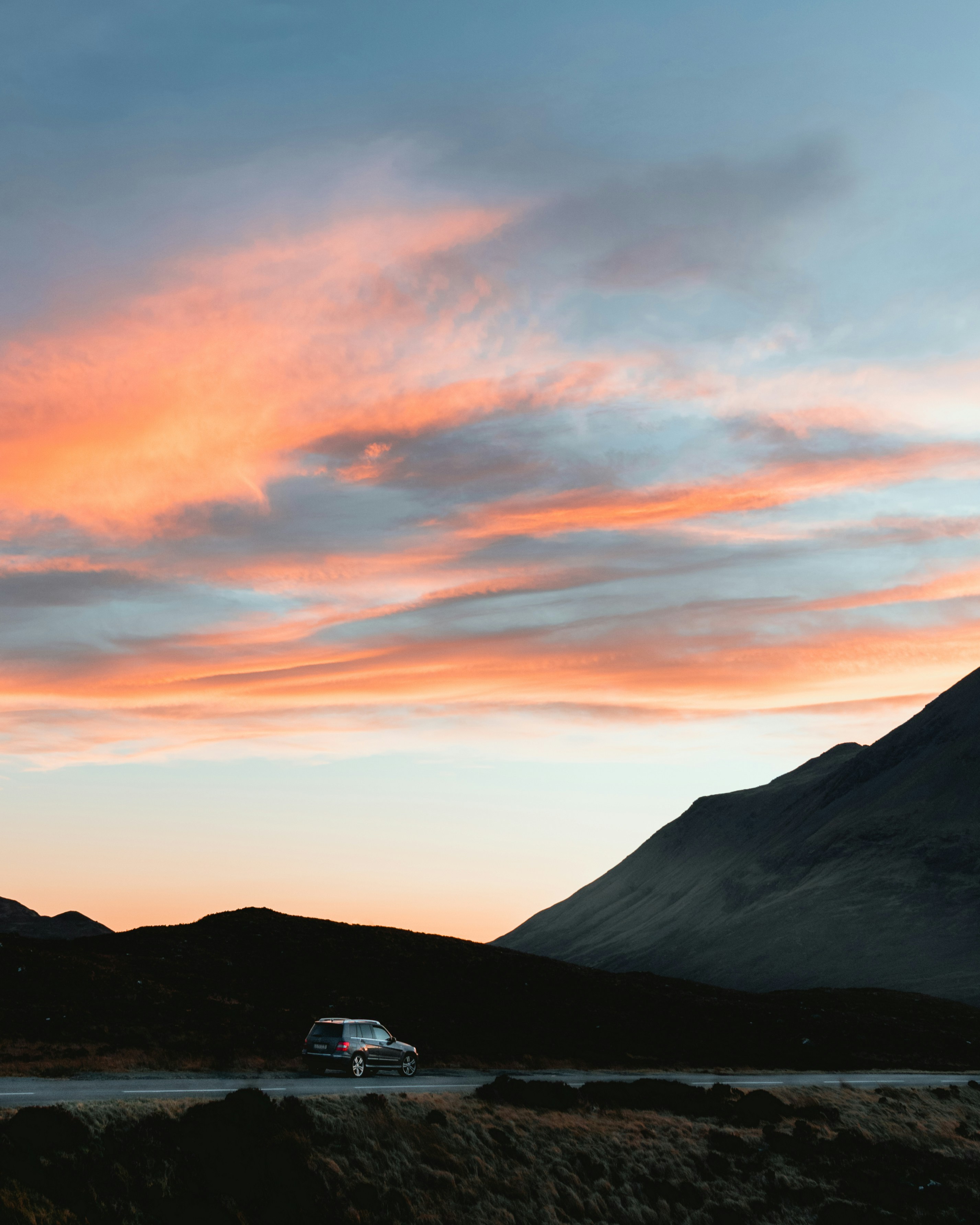 Car on a Quiet Sunset Road Beneath Coral Clouds and a Shadowed Mountain