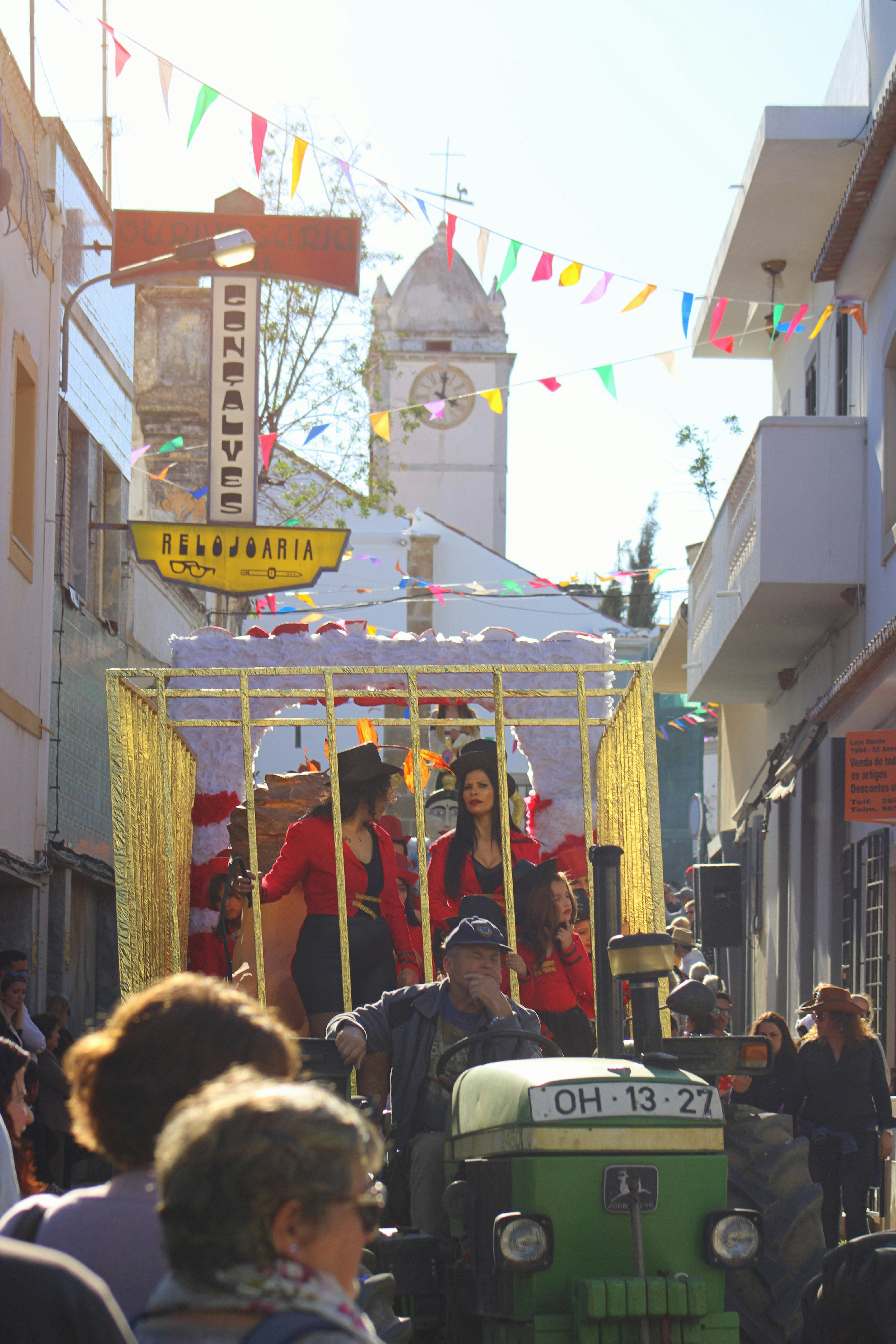 Vibrant parade featuring performers in red attire, framed by colorful decorations and a historic clock tower in the background.