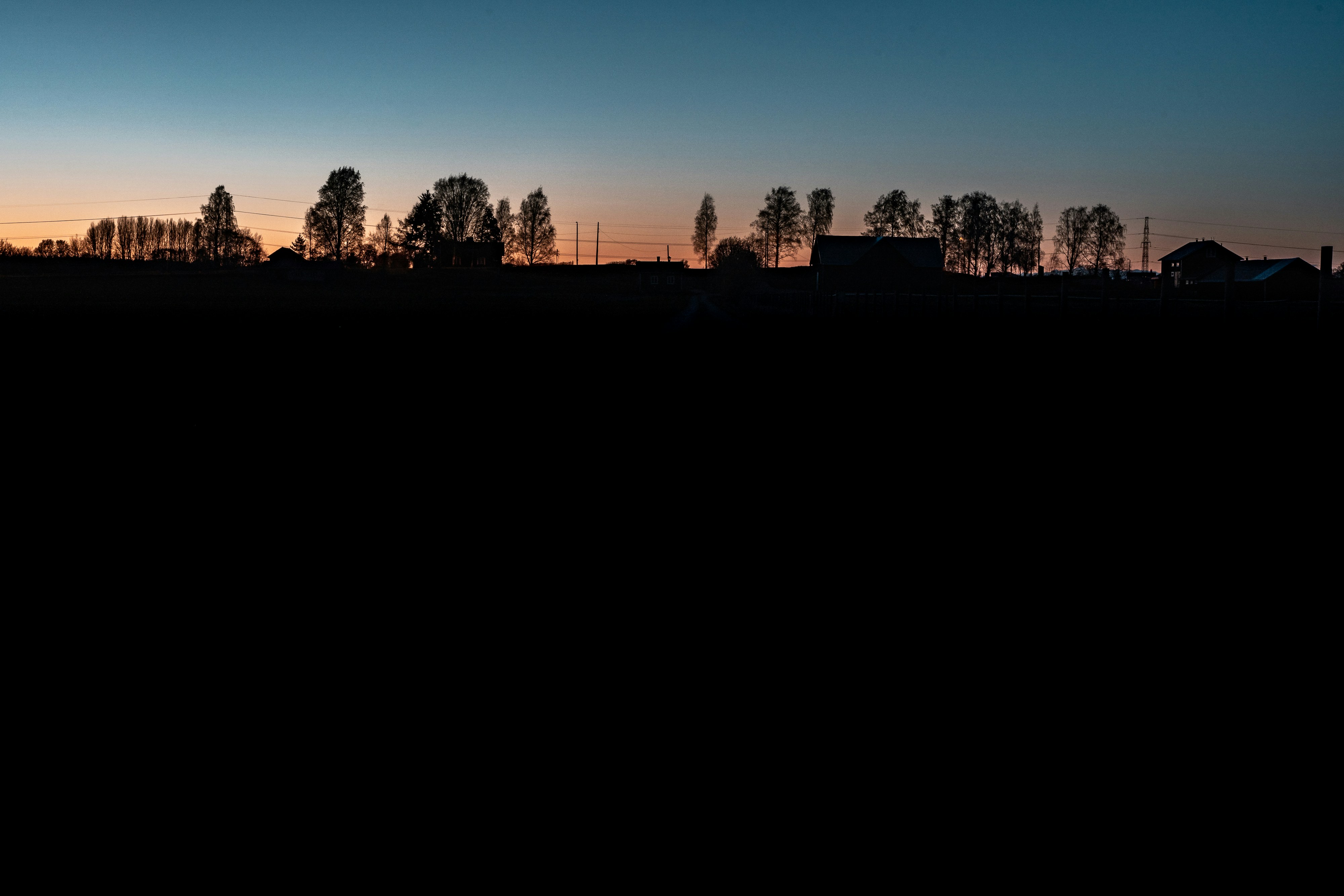 Silhouettes of trees and buildings against a gradient sky at twilight, creating a serene and tranquil landscape.