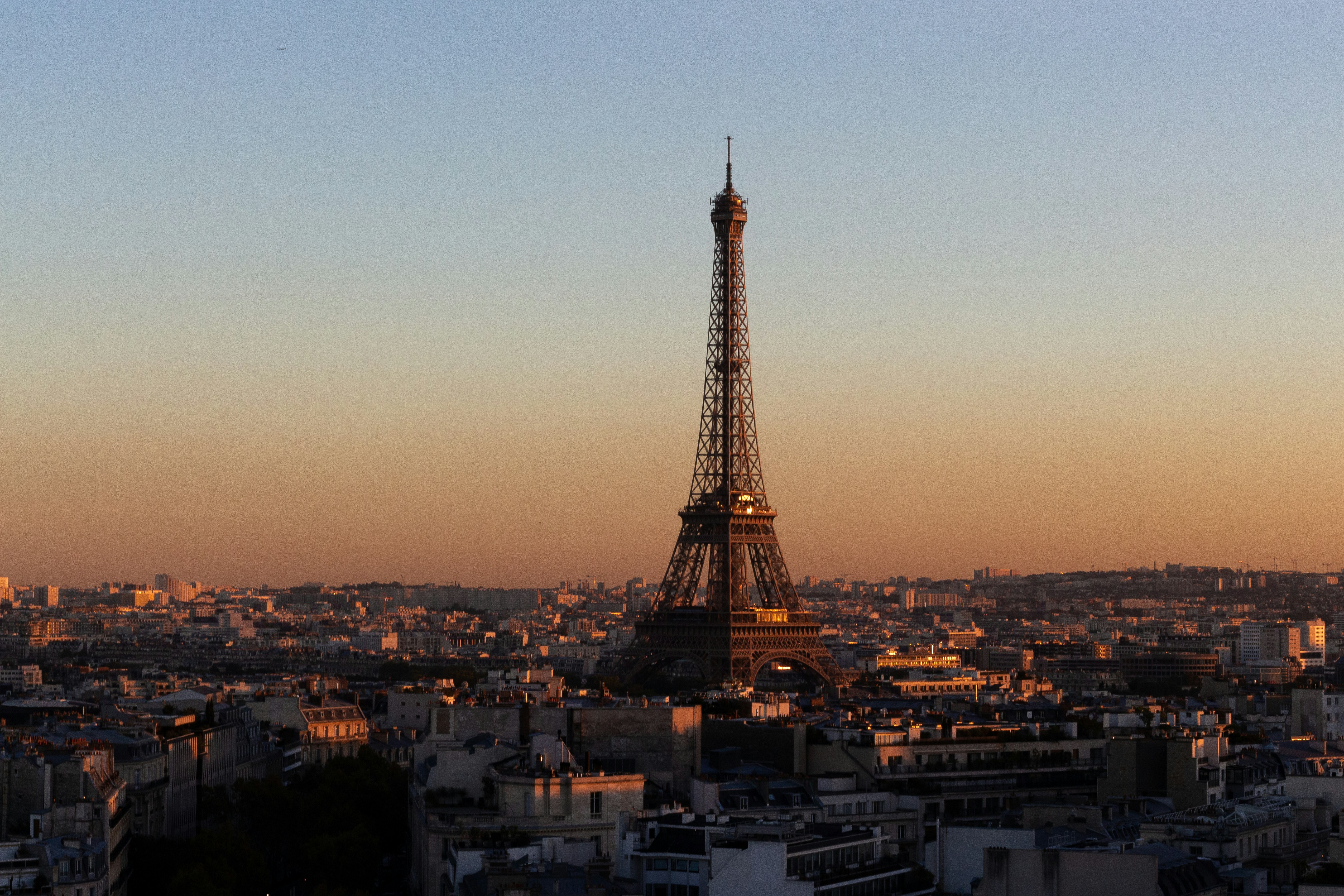 Eiffel Tower silhouetted against a warm sunset, overlooking the Parisian skyline. The scene captures the essence of the city's romantic allure.