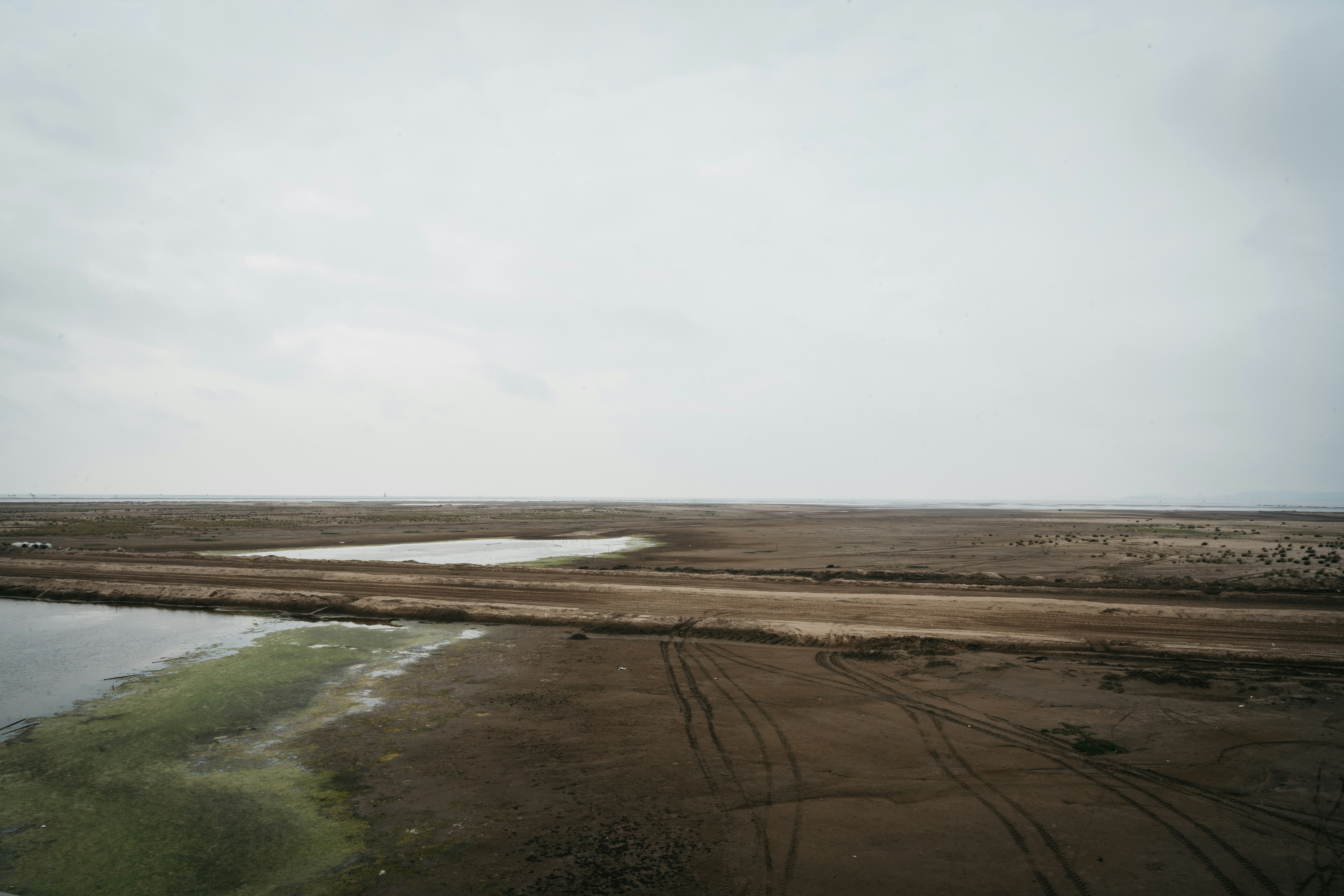 Expansive salt flats under a cloudy sky with distant water pools breaking the barren landscape.