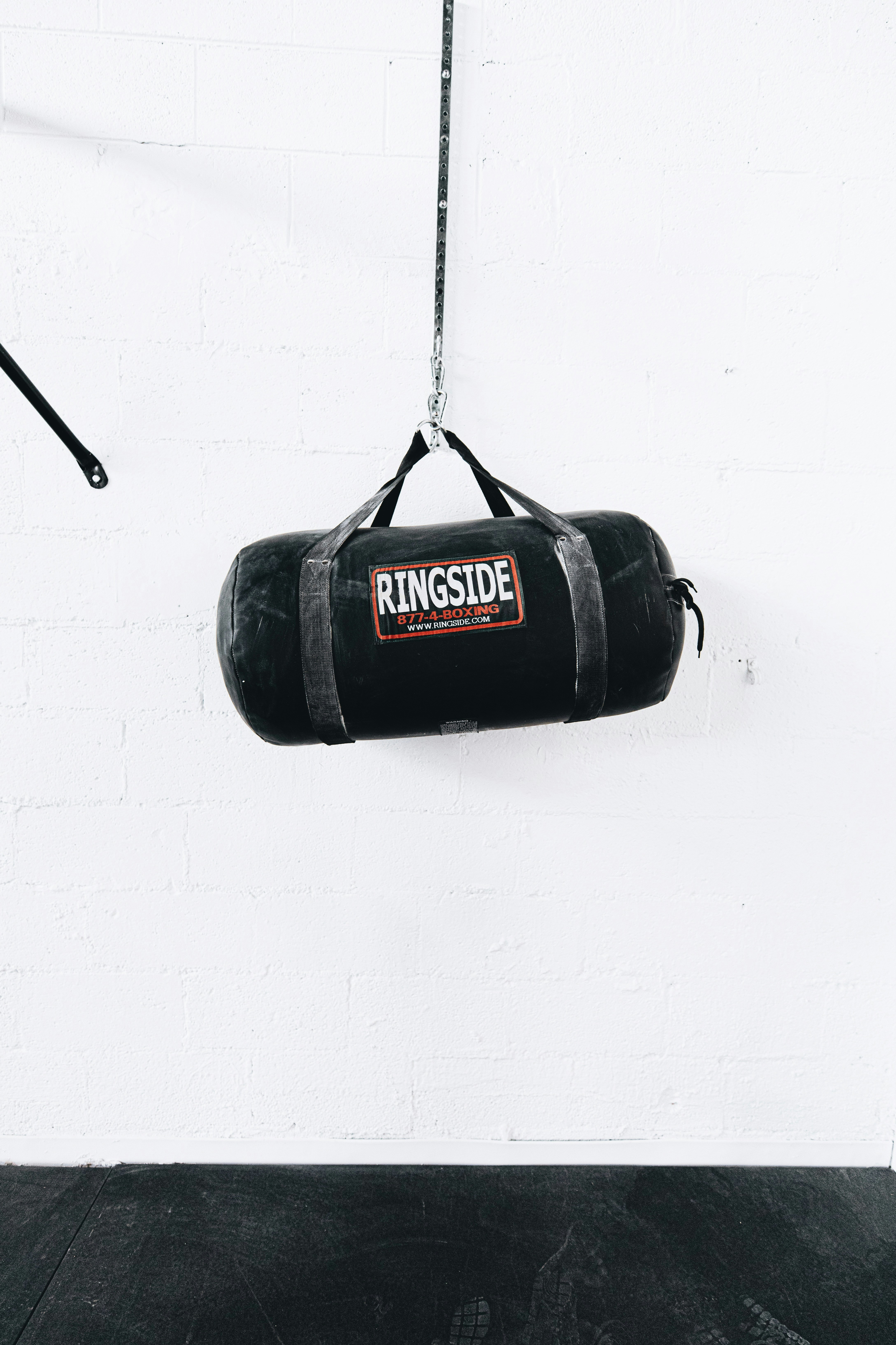 A hanging black punching bag against a minimalist white wall, emphasizing the dedication required in boxing training.