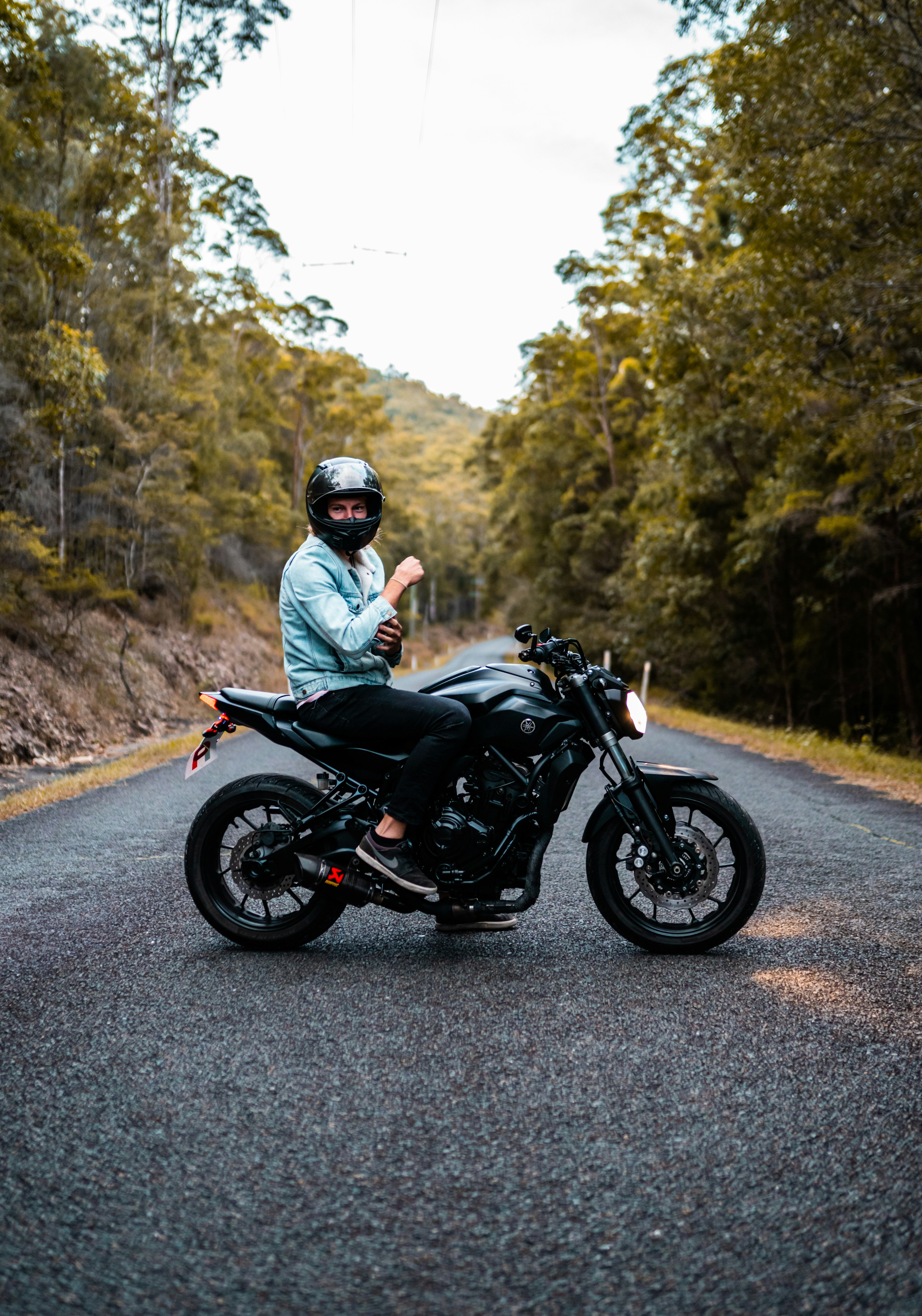 Mid-forest ride: rider astride a matte-black motorcycle on a quiet forest road