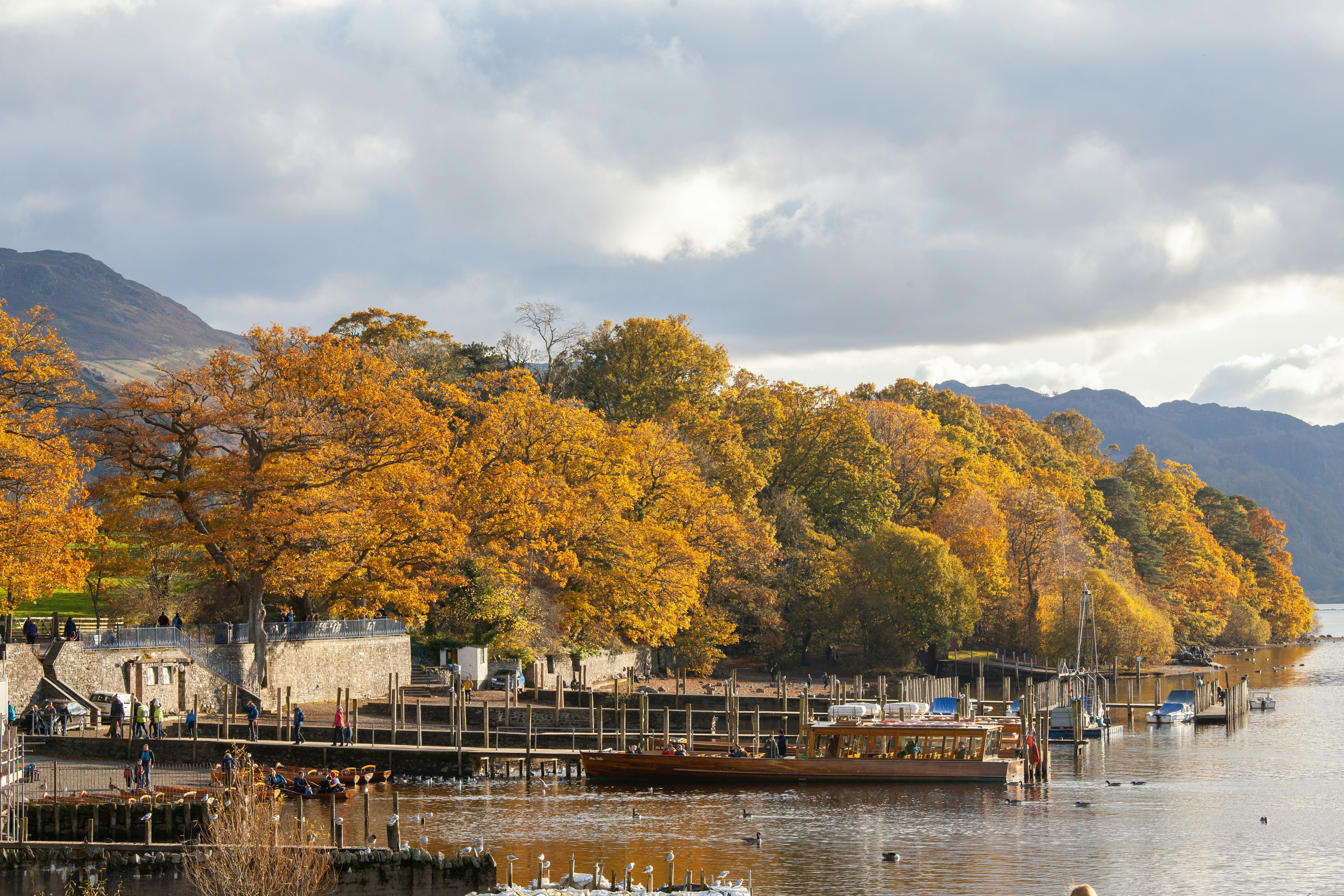 Vibrant autumn foliage reflects on the serene waters of a lakeside dock, with boats gently bobbing in the foreground.