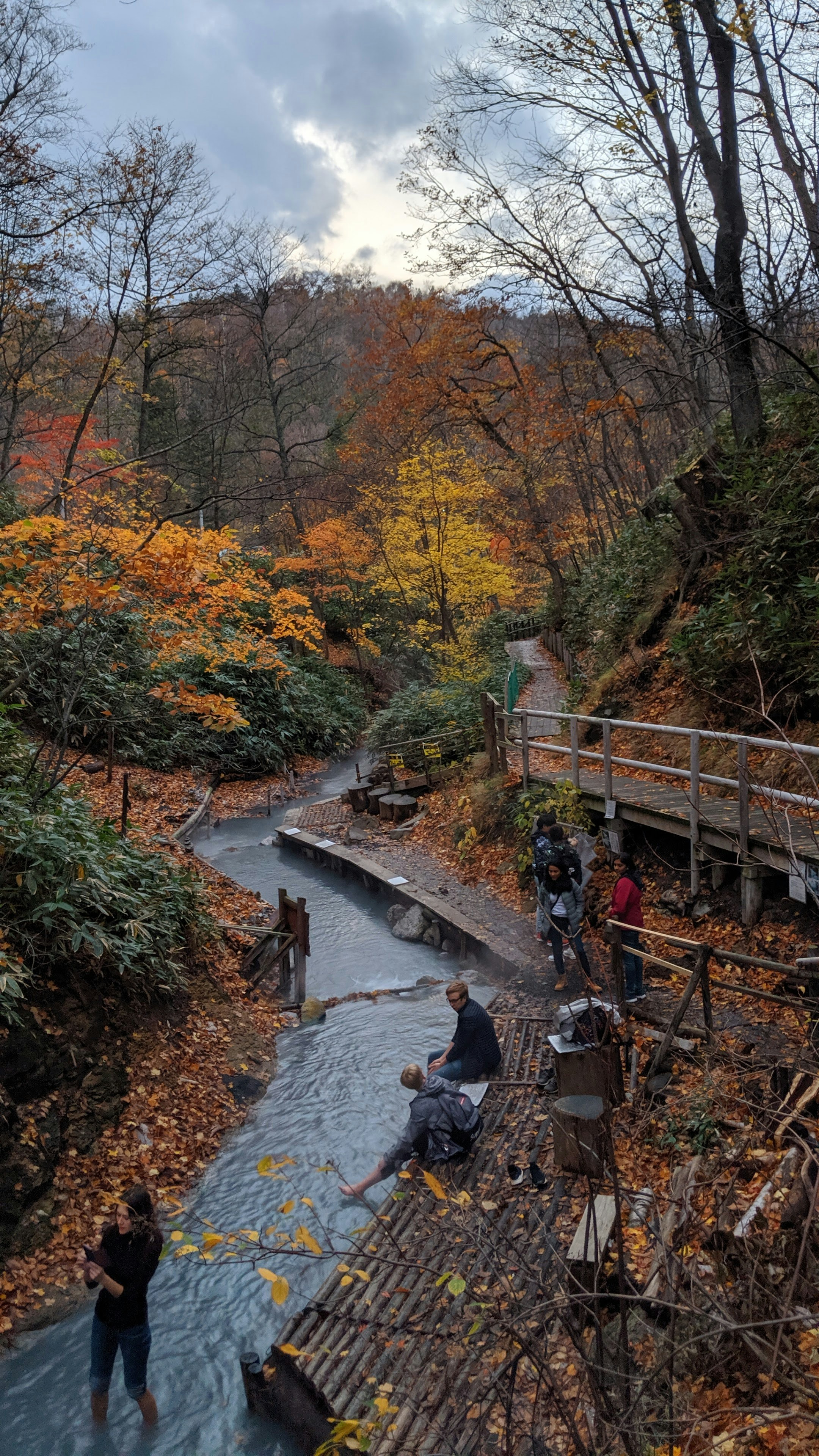 Autumn Riverwalk: Hikers Along a Turquoise Stream Under a Leafy Canopy