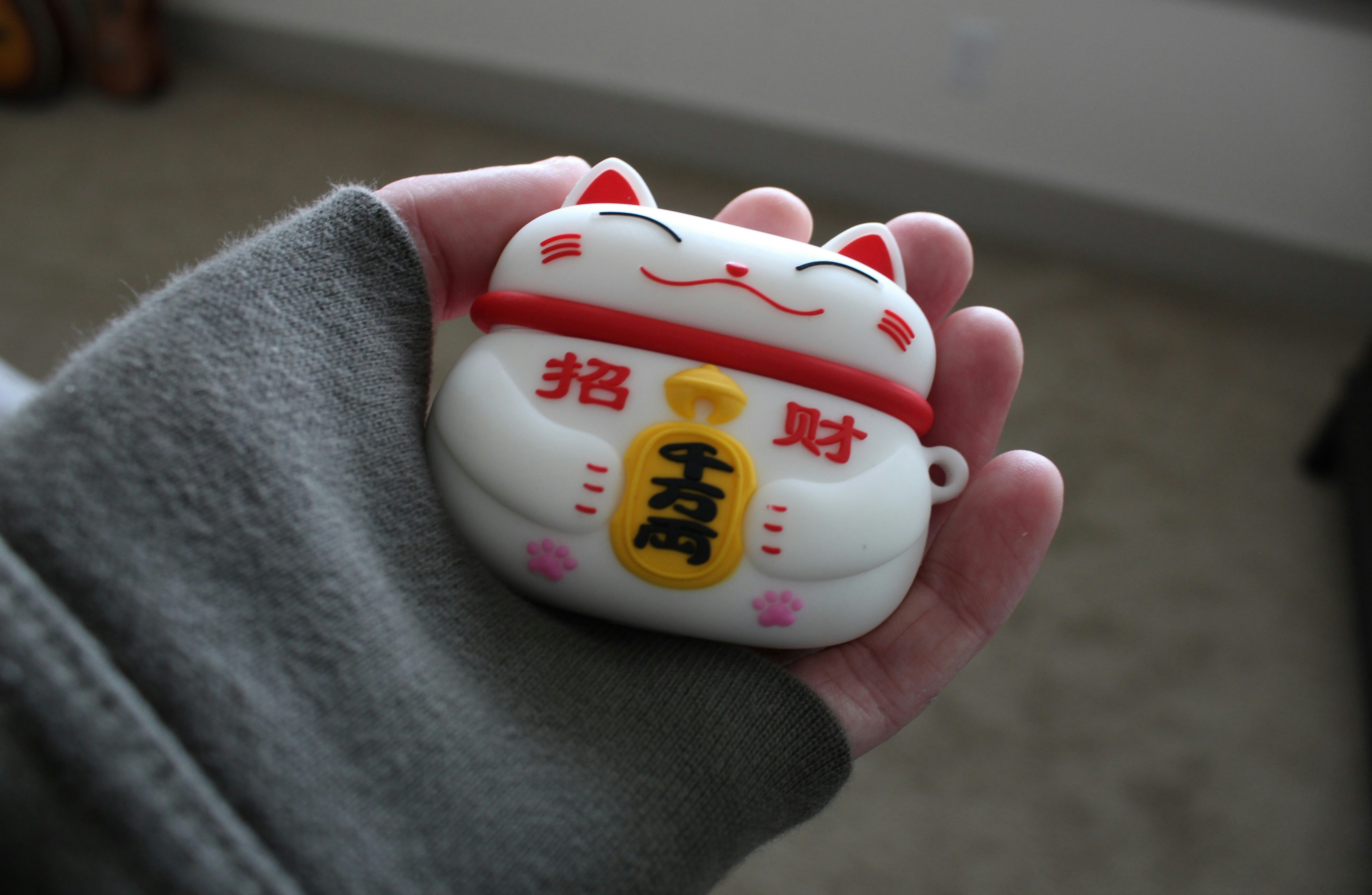 A hand cradles a white Maneki-neko figurine adorned with red accents and Japanese inscriptions, symbolizing good fortune and prosperity.