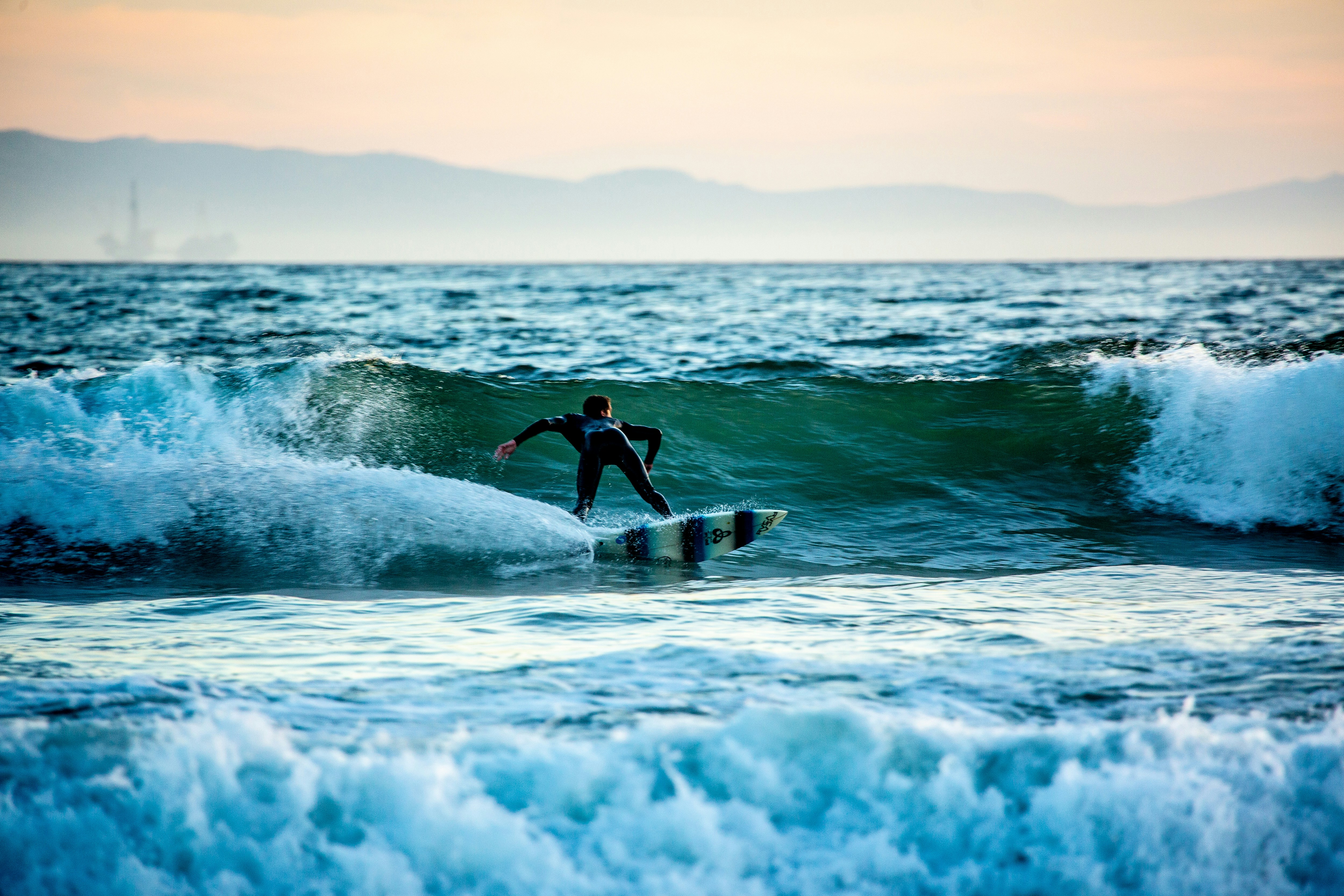 Surfer carving through a wave at sunrise with distant mountains in view.