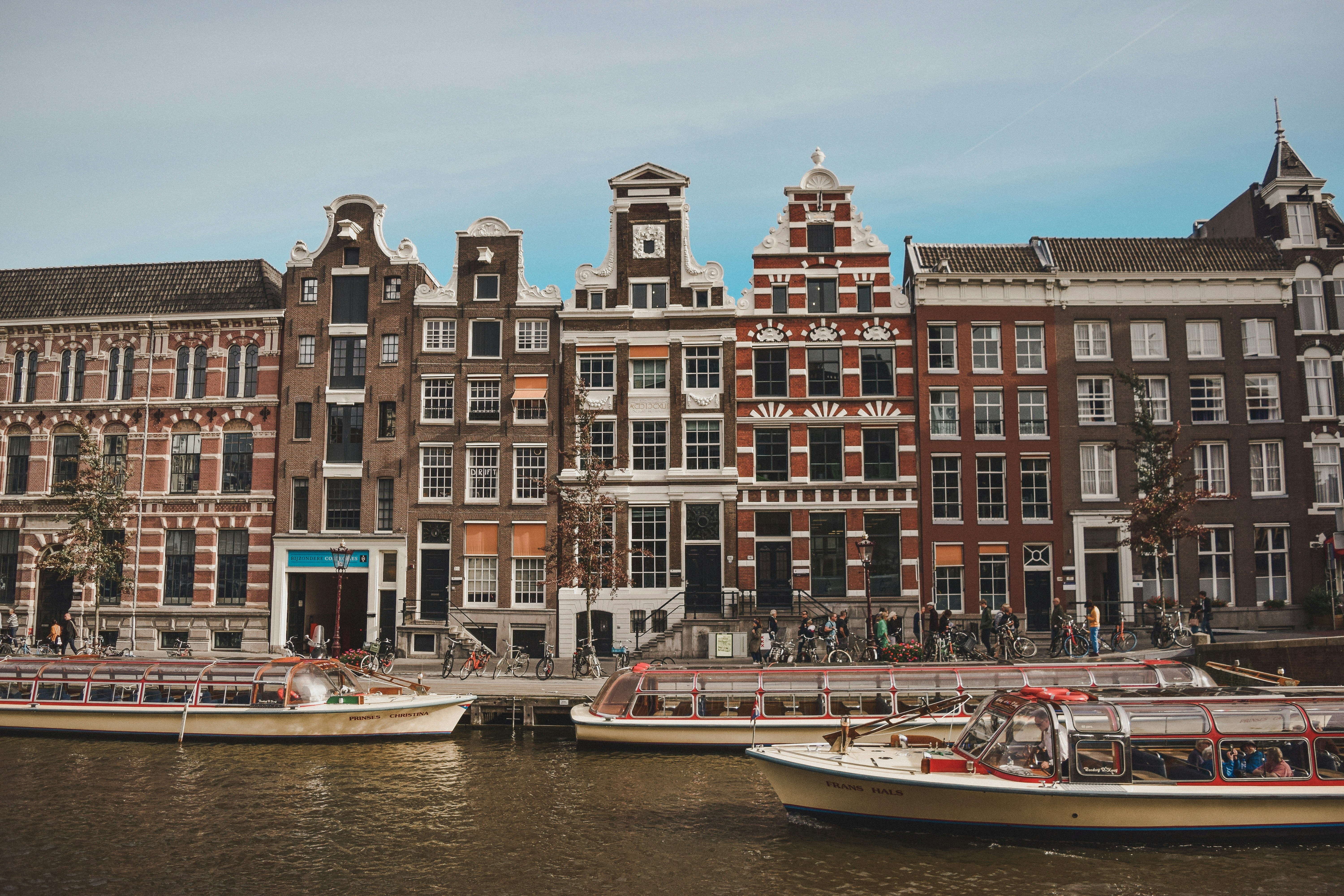 Colorful canal houses line the waterfront in Amsterdam, with boats docked nearby and people enjoying the vibrant atmosphere.