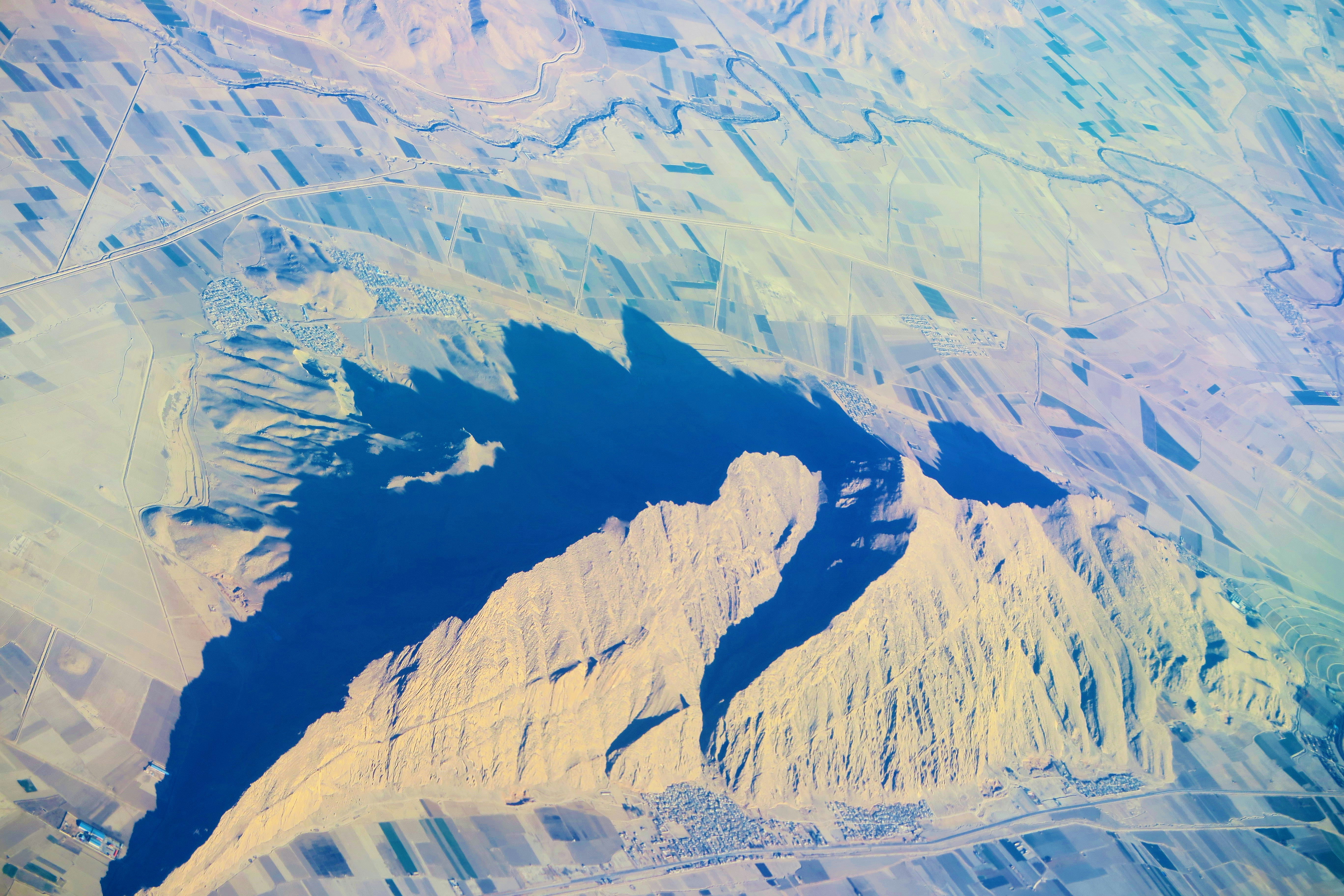 Aerial view of a winding body of water bordered by rugged mountains and agricultural fields, showcasing the interplay of land and water.