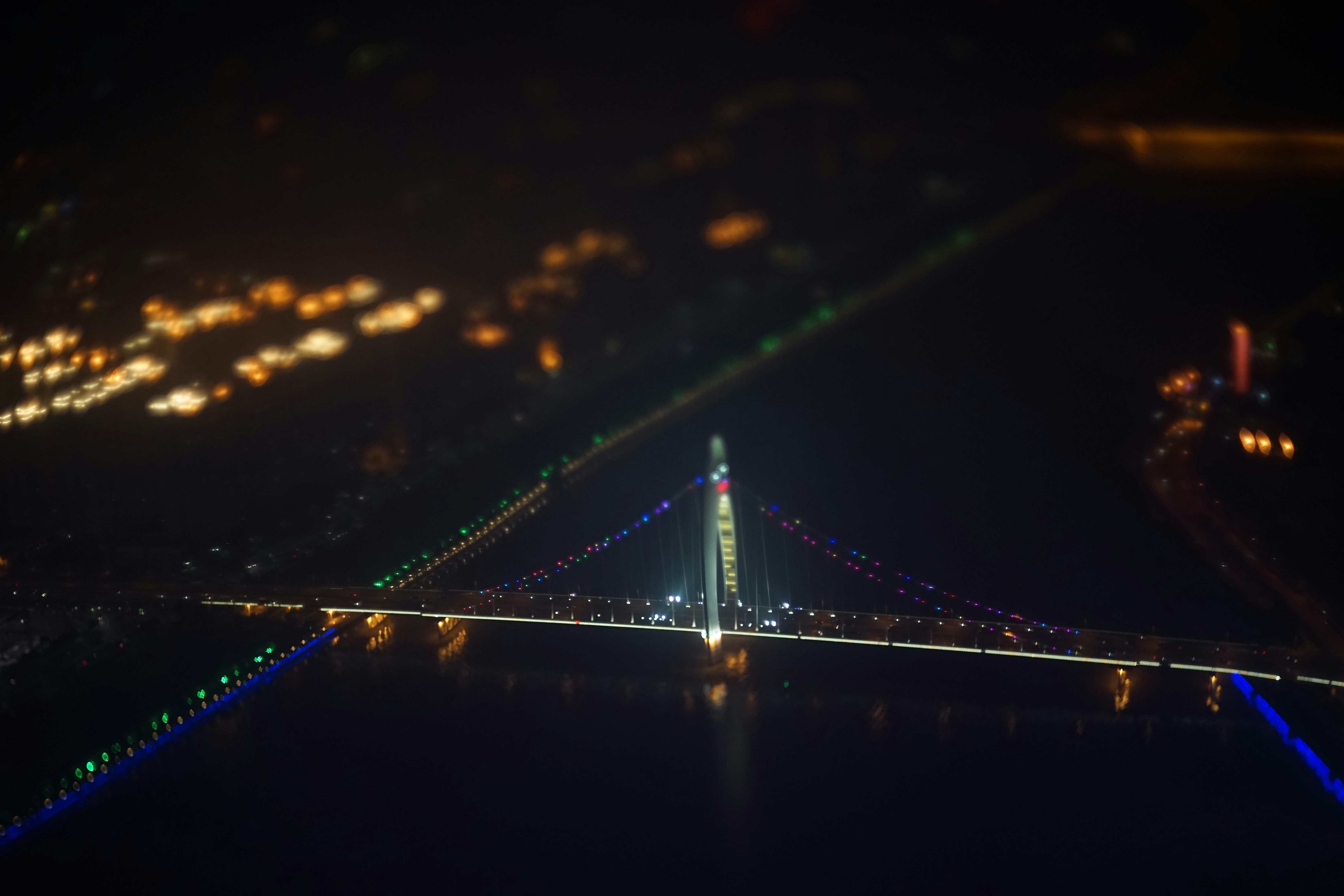 Rainbow-lit suspension bridge at night crossing a dark river