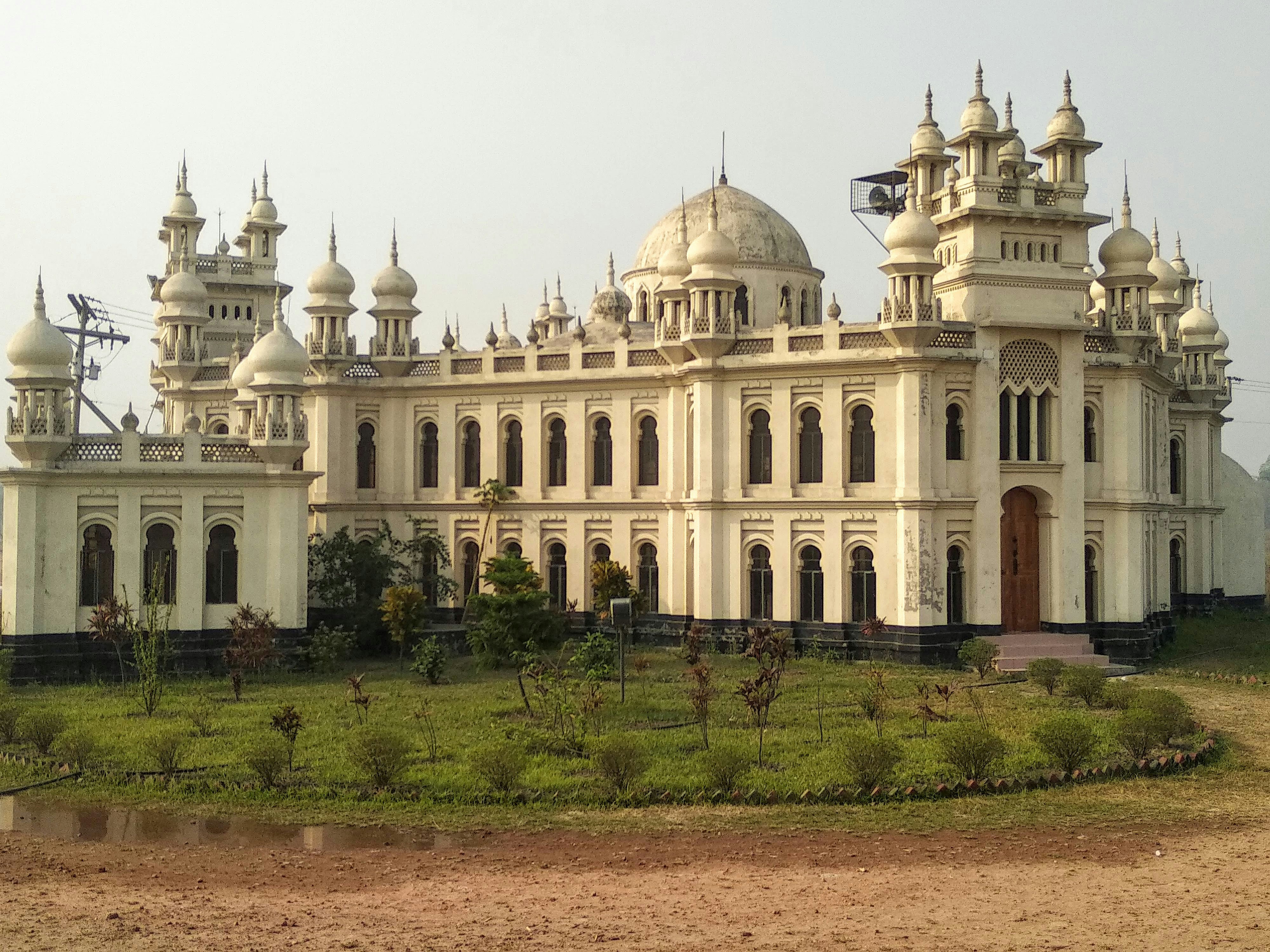 White building with multiple domes and spires surrounded by a grassy courtyard.