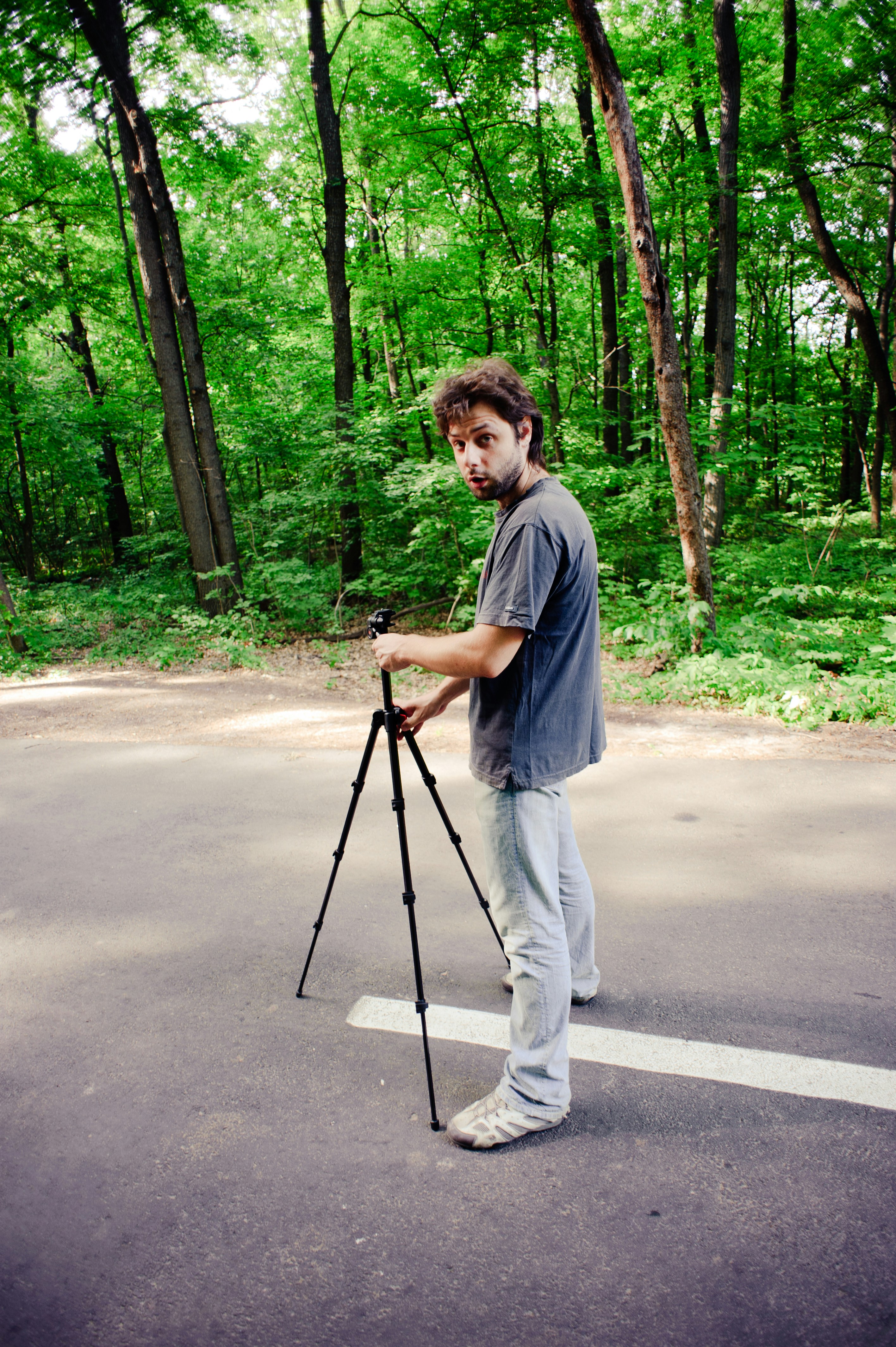 Photographer adjusting a tripod on a forest road surrounded by lush greenery.