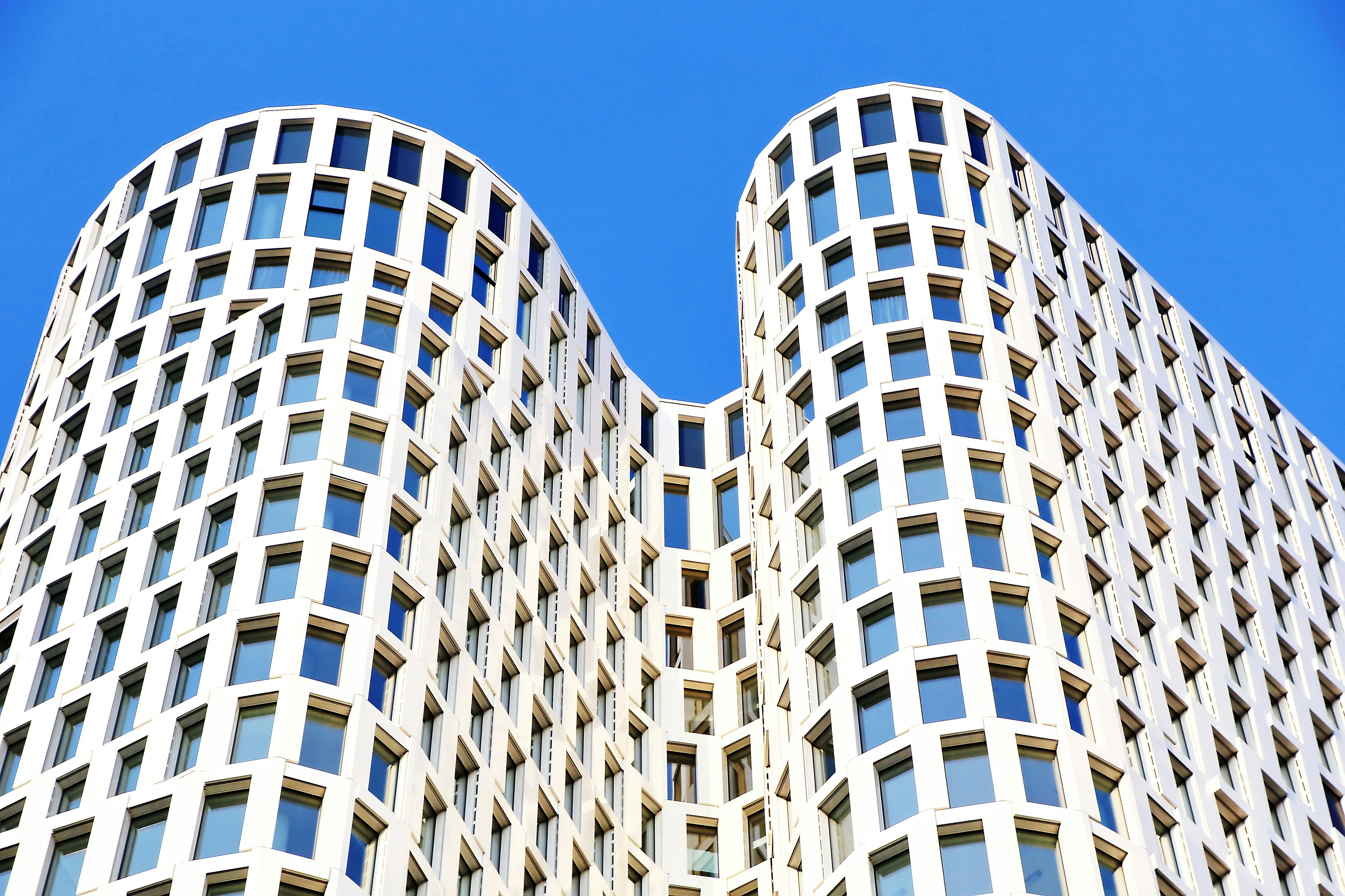 Wavy, modern building facade with a grid of windows against a clear blue sky.