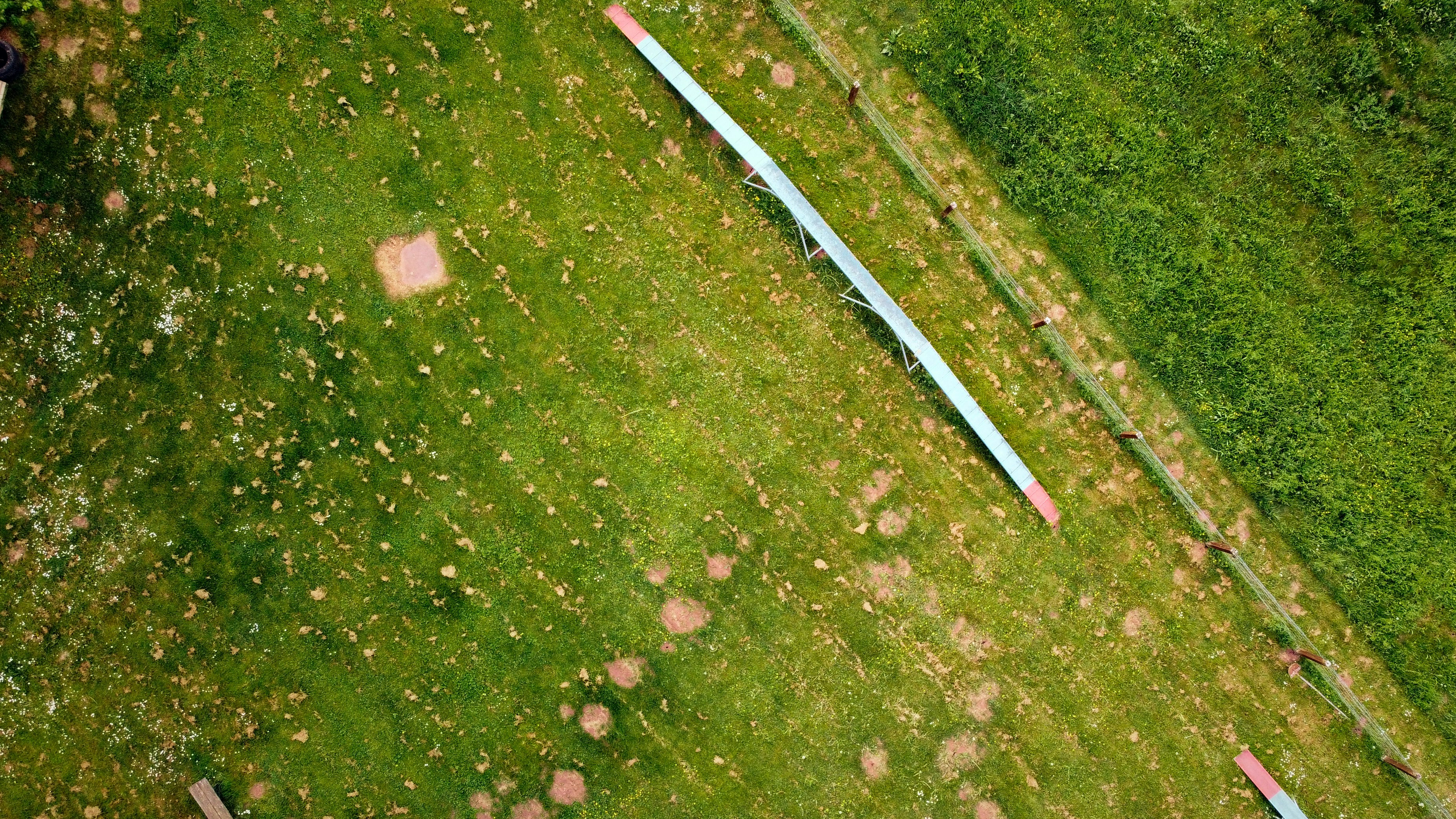 Aerial view of a long, metal structure dividing lush green fields with patches of brown soil.