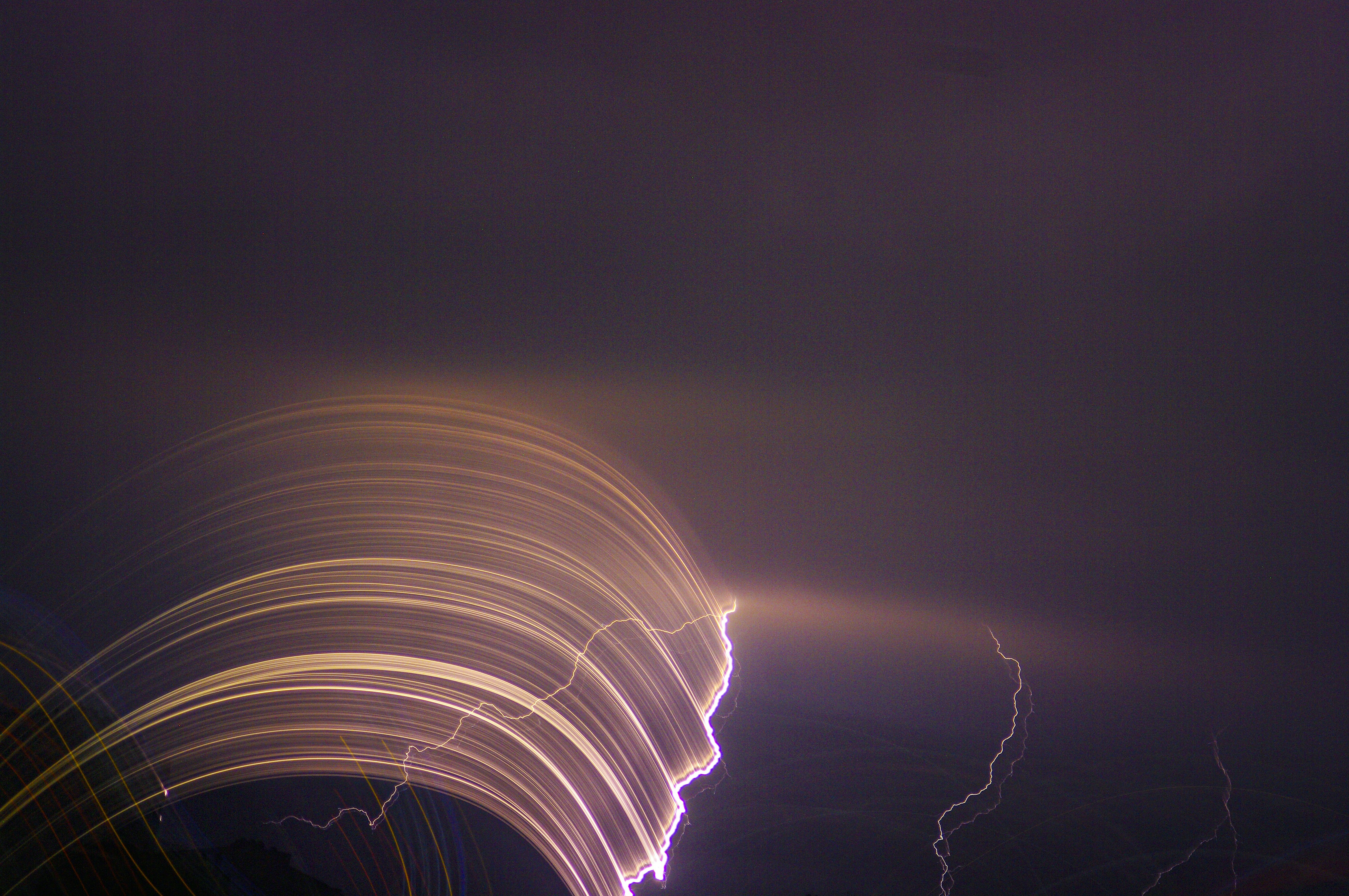Long-exposure night photograph capturing looping light trails and a jagged lightning bolt across a stormy sky.