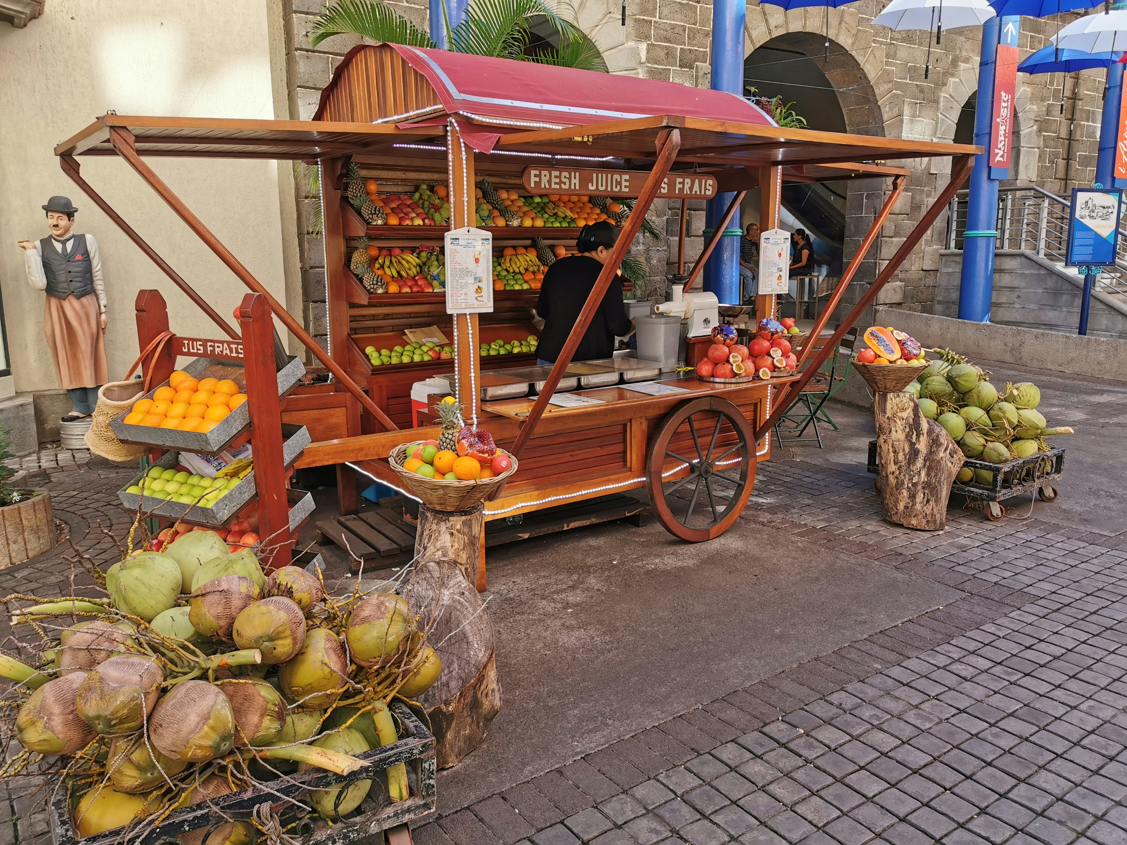 Colorful fruit juice stand brimming with fresh produce, surrounded by coconuts and vibrant decorations. A lively scene in a bustling market.
