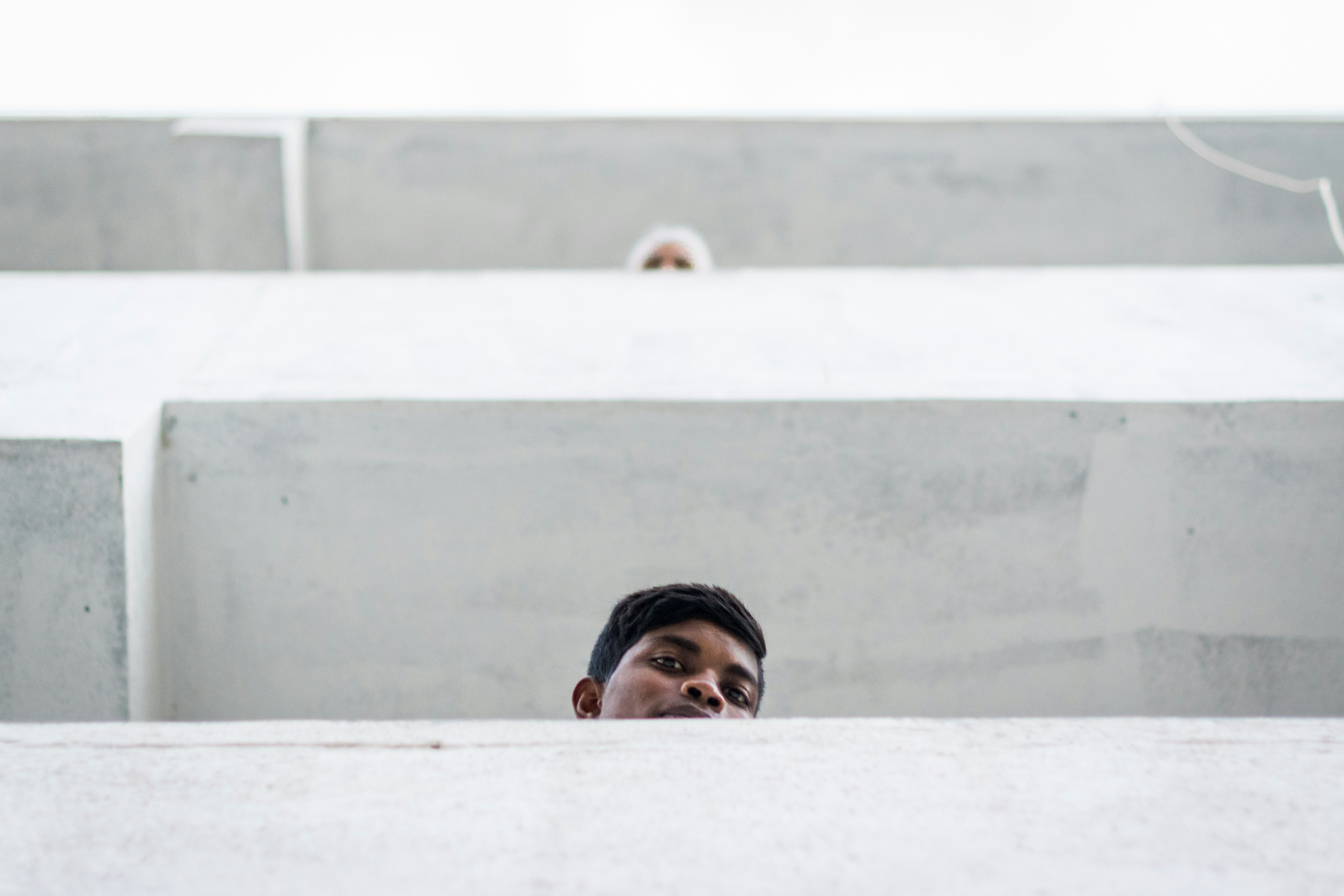 Person looking down from a high concrete balcony with white geometric lines.