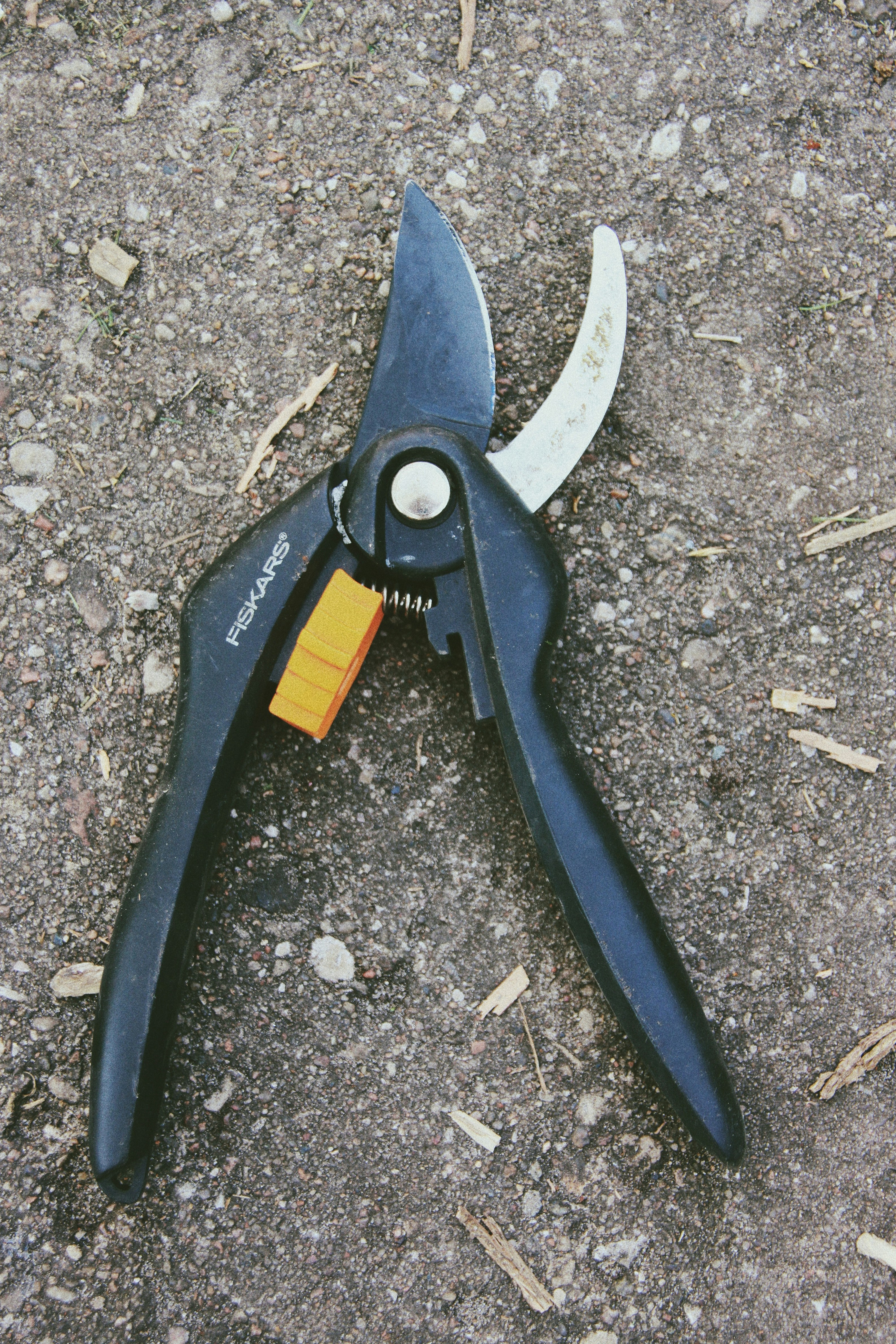 Black pruning shears resting on a gravel surface, showcasing their design and functionality.