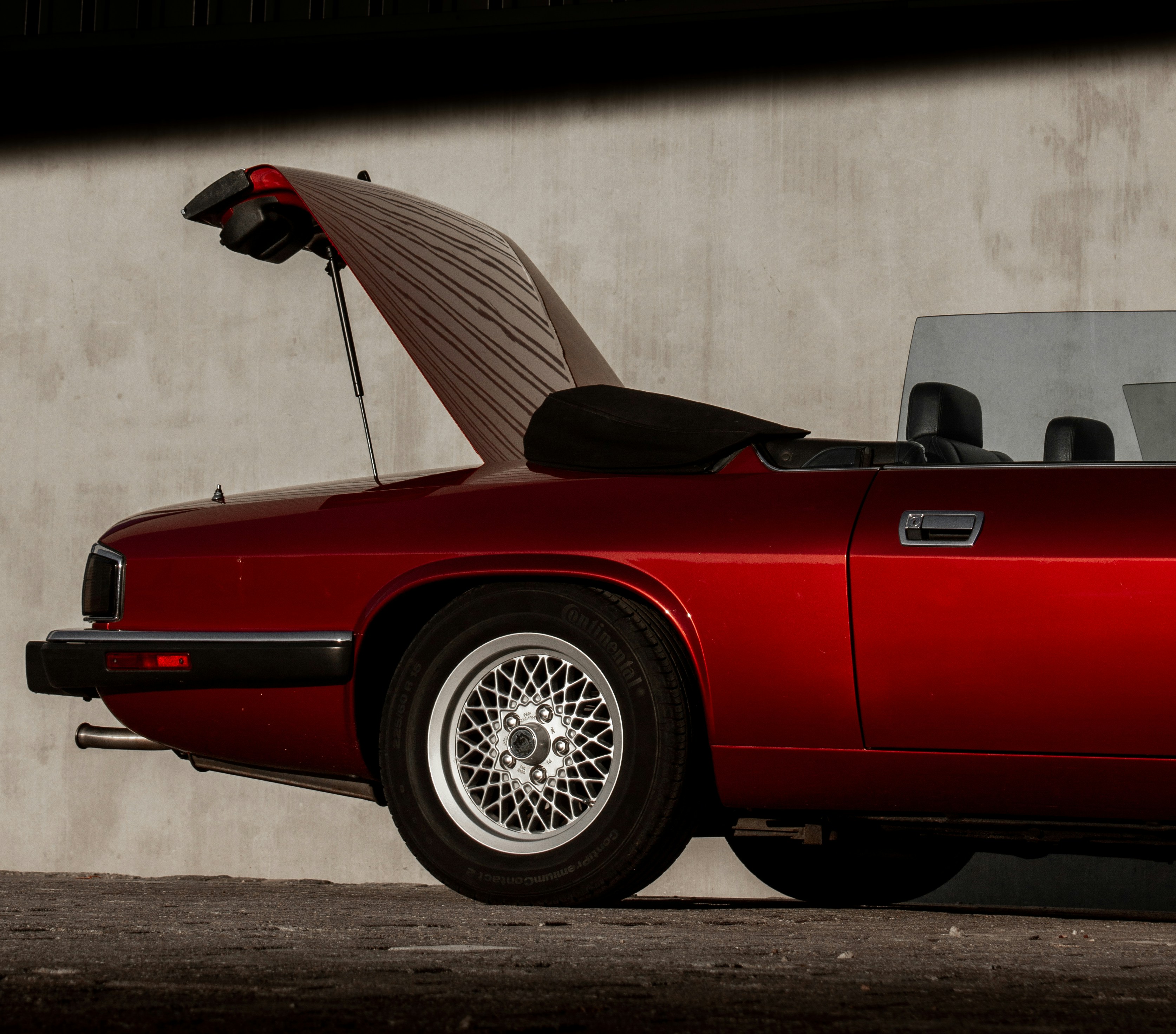 Classic red convertible with its trunk open against a minimalist concrete wall.