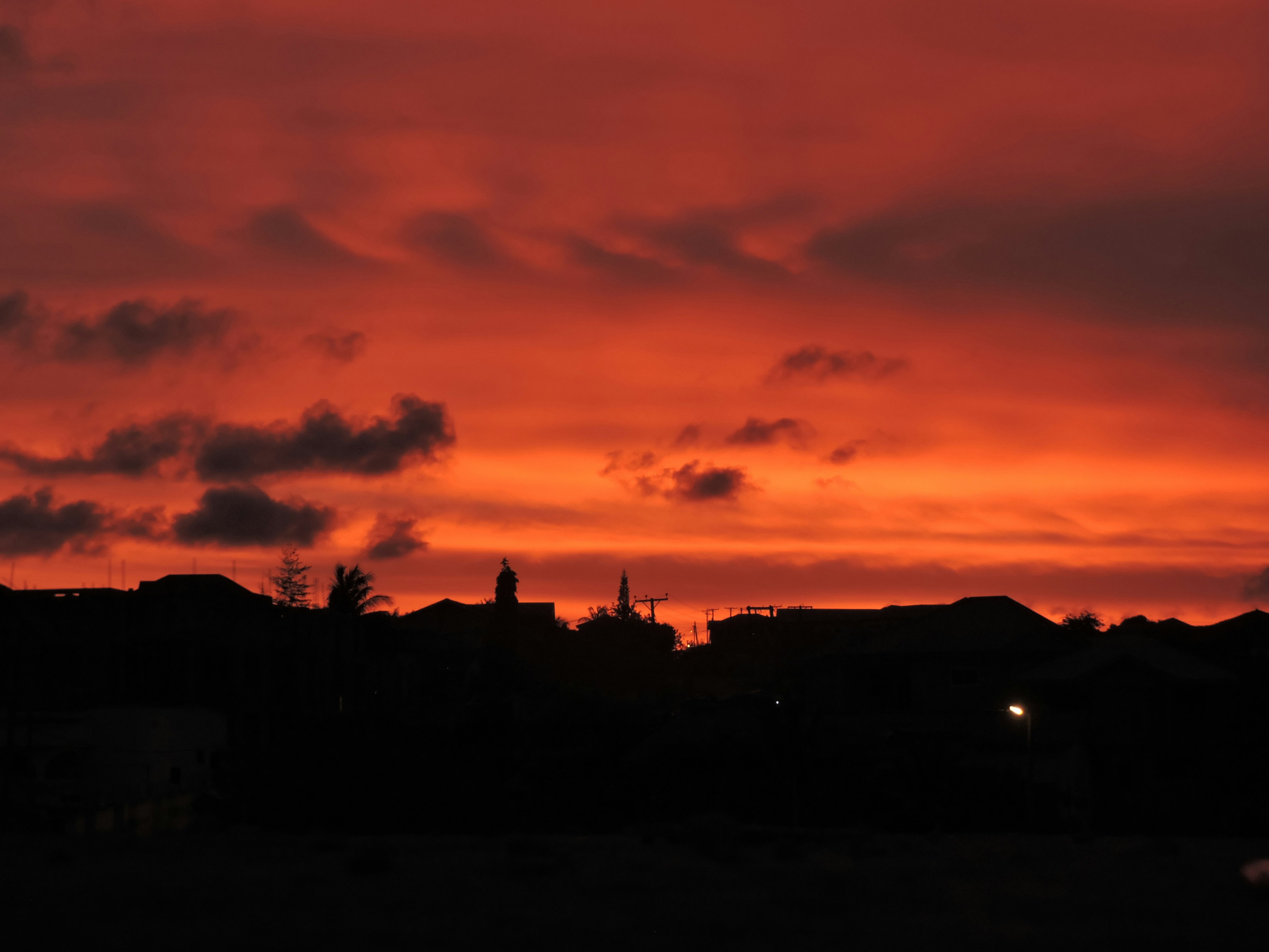Fiery red sky at sunset with dark building silhouettes in the foreground.