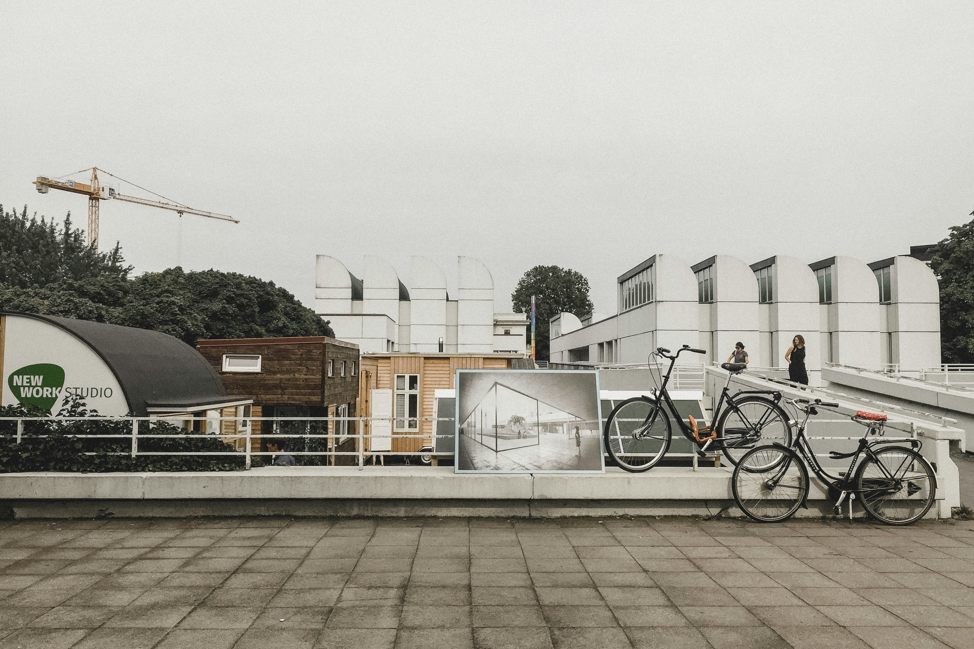 Bicycles resting on a platform in an urban setting, framed by modern architecture and a construction crane in the background.