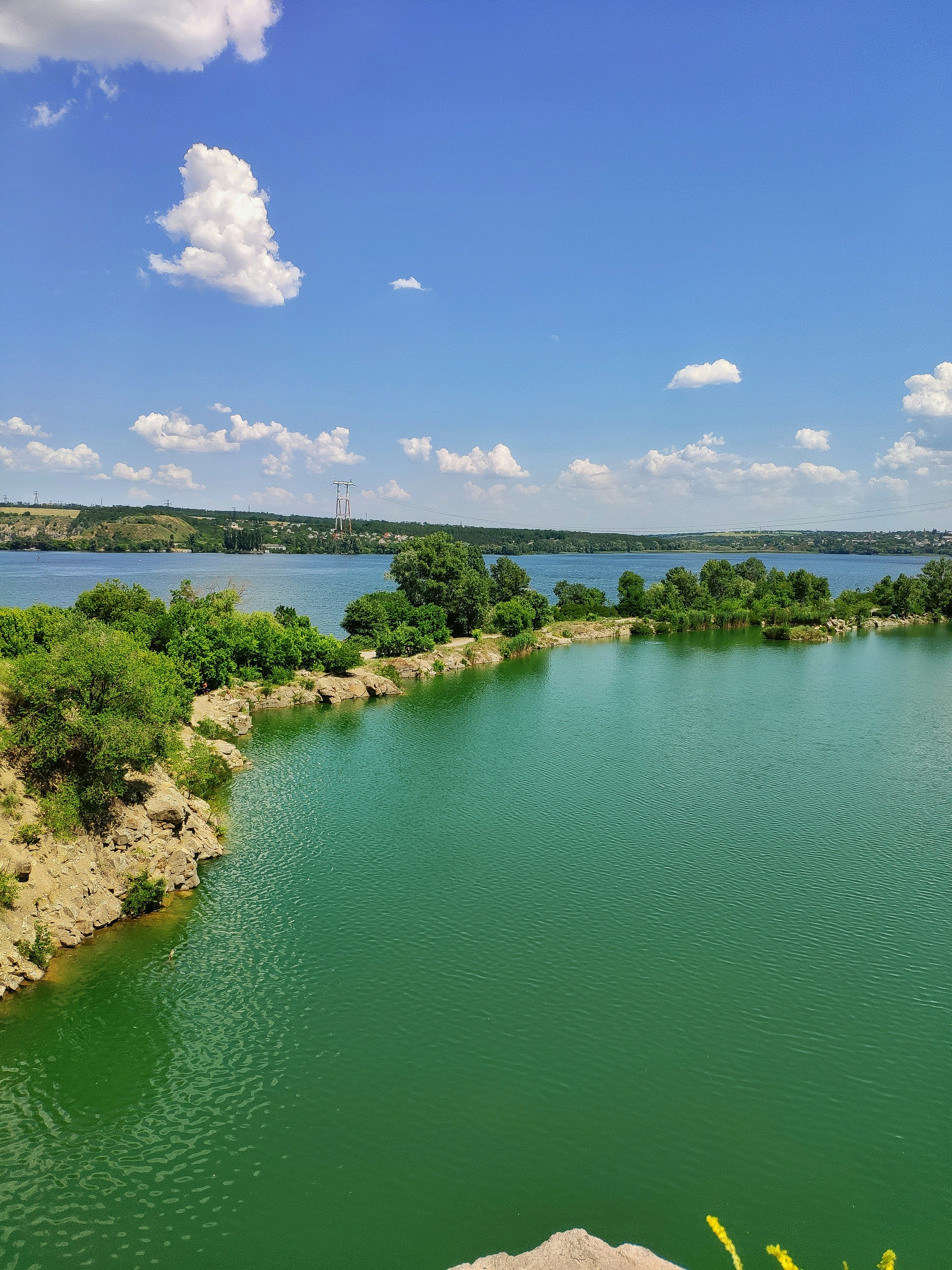 Vibrant green water reflecting a clear blue sky, framed by lush greenery and rocky shores. A serene landscape inviting exploration.
