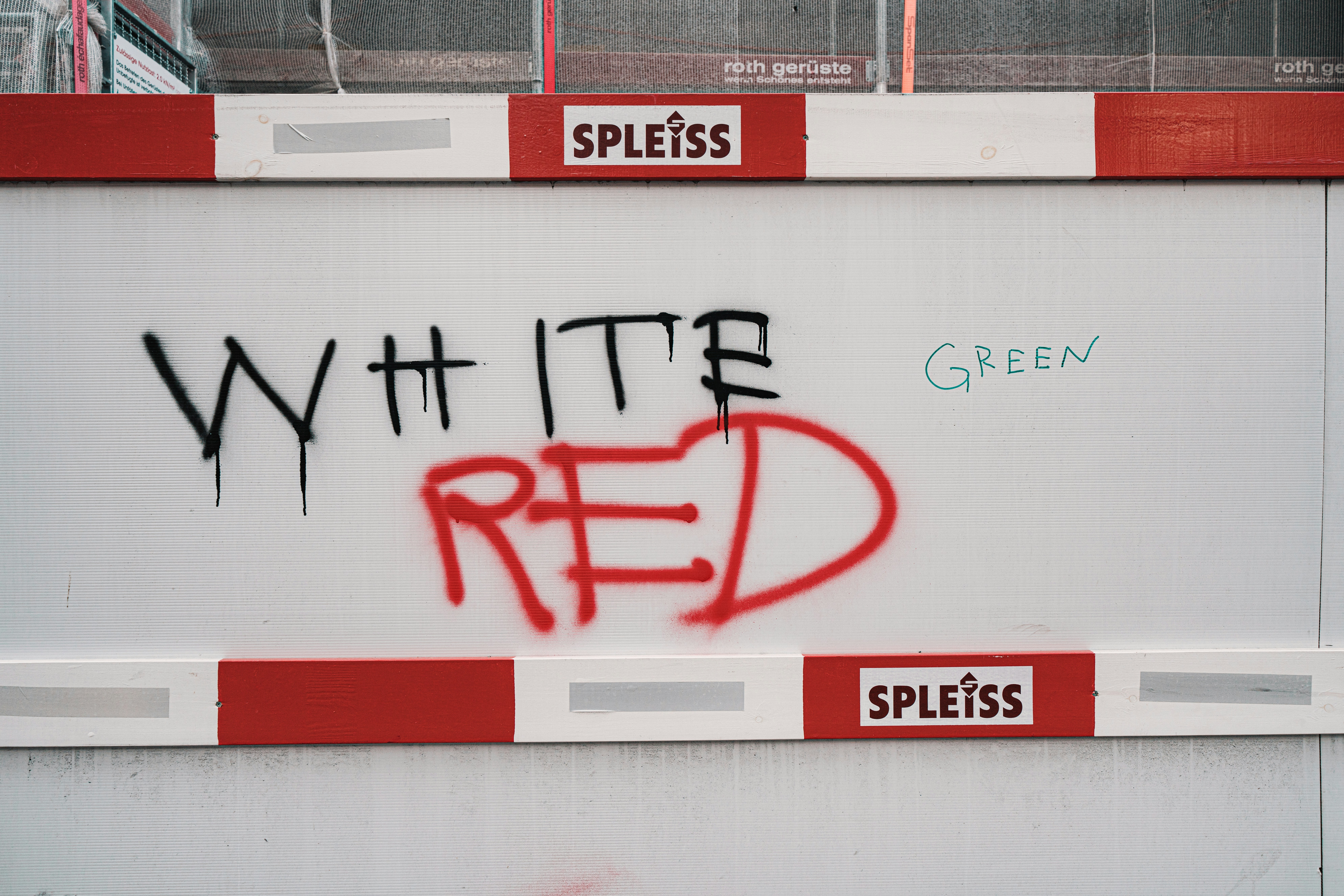 Crimson Graffiti on a Stark White Barrier Beneath Industrial Rails