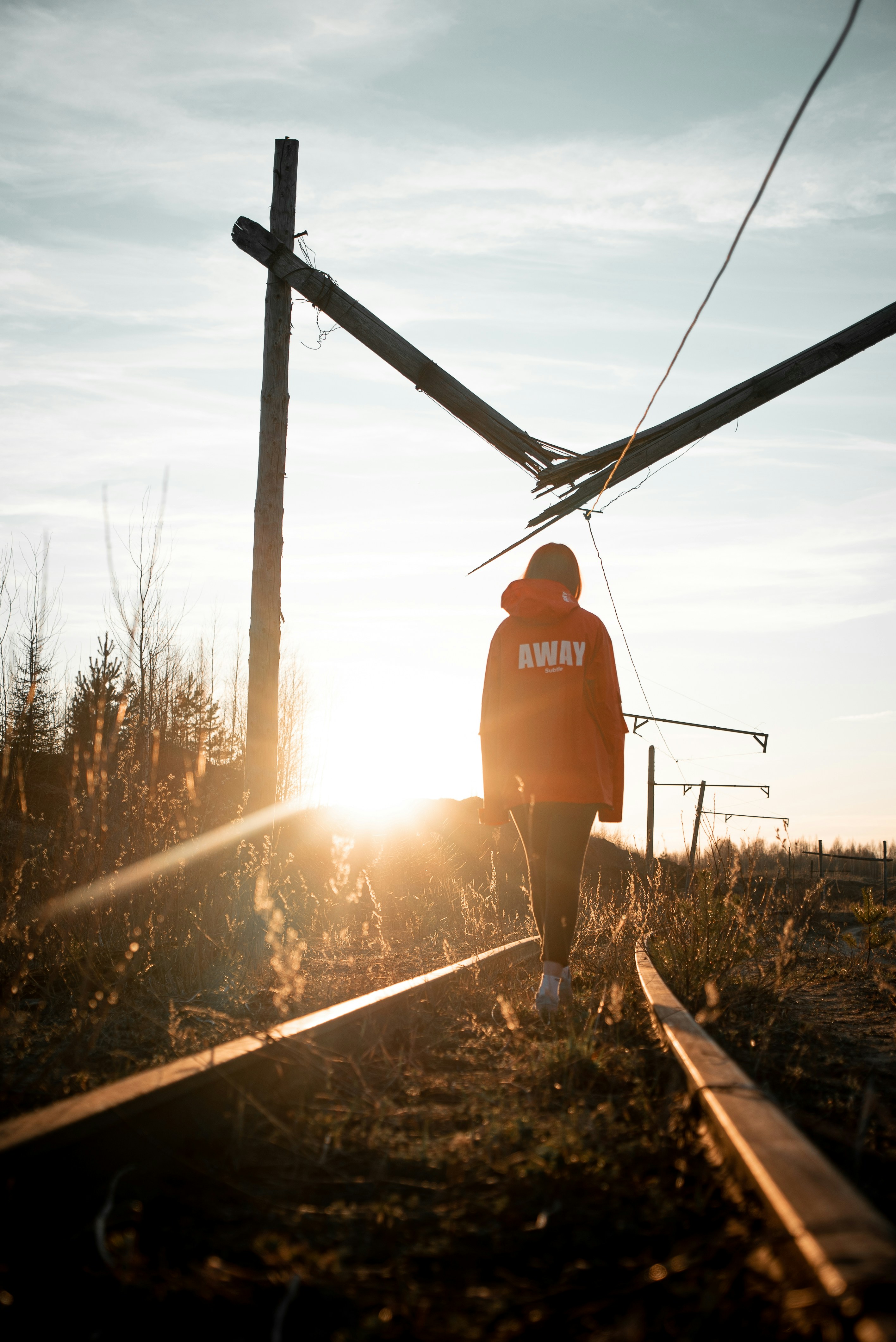 Backlit Awakening: A figure in an orange hoodie on rusted rails at sunset
