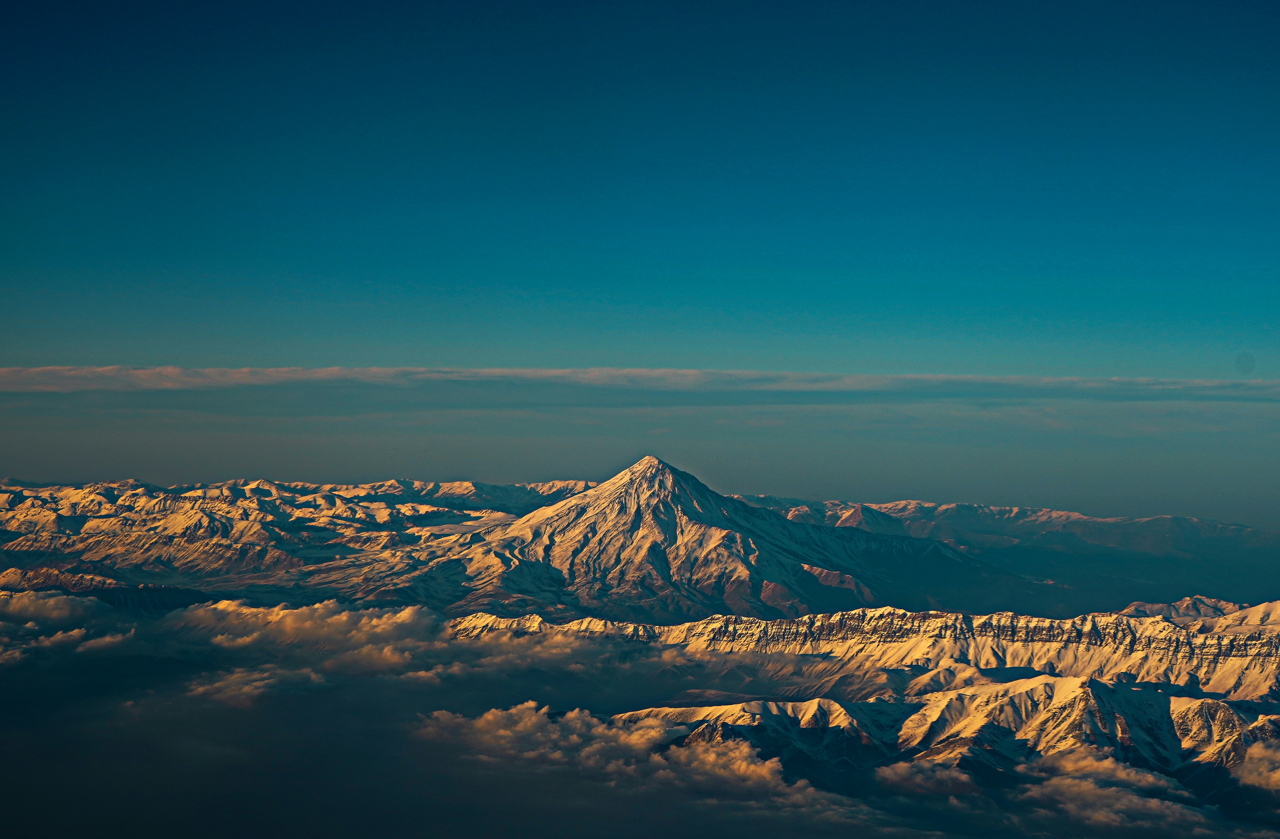 Snow-covered Damavand Peak rises under a clear blue sky during daylight.
