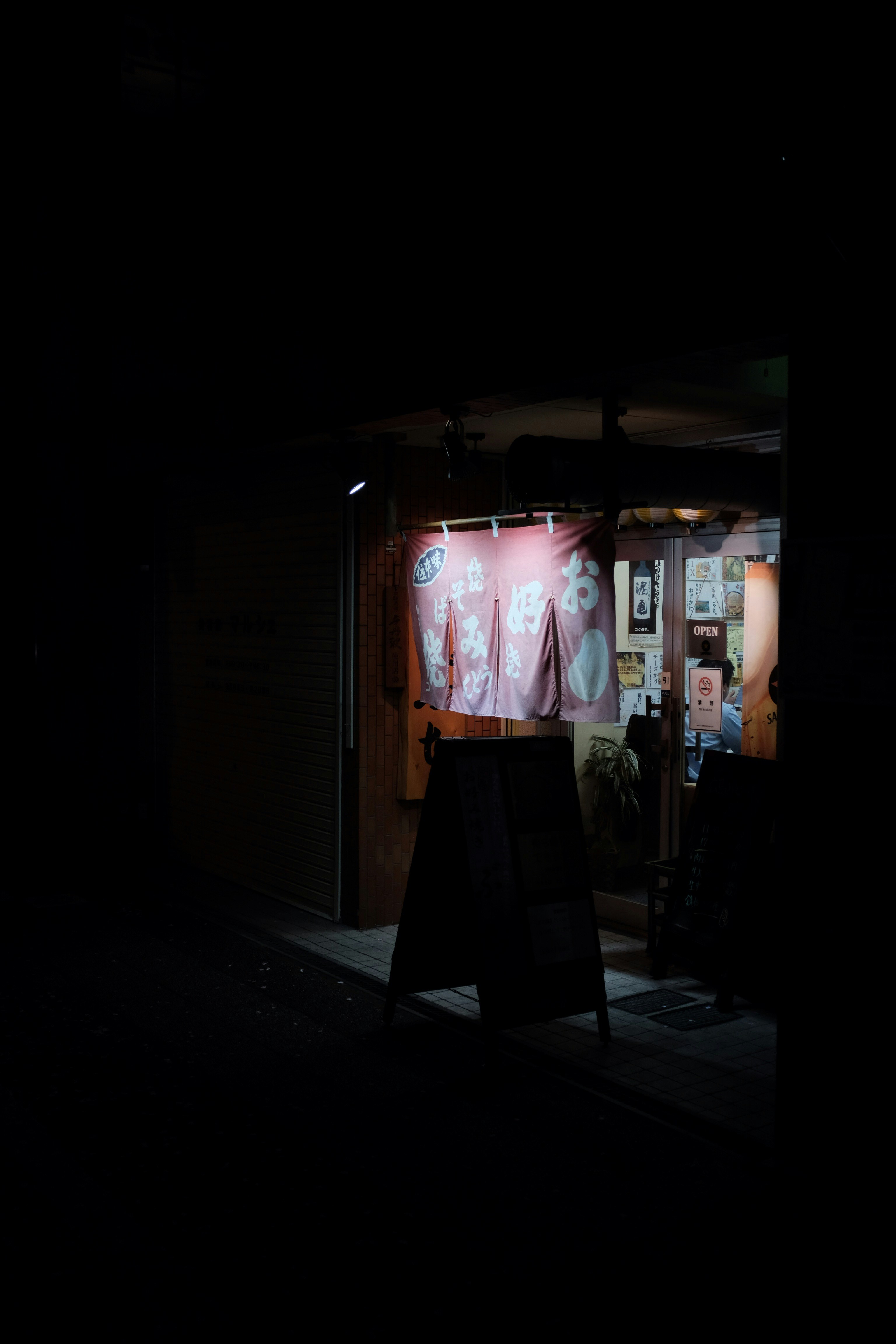 Neon-lit restaurant entrance with traditional fabric banners and a welcoming 'OPEN' sign, set against a darkened street backdrop.