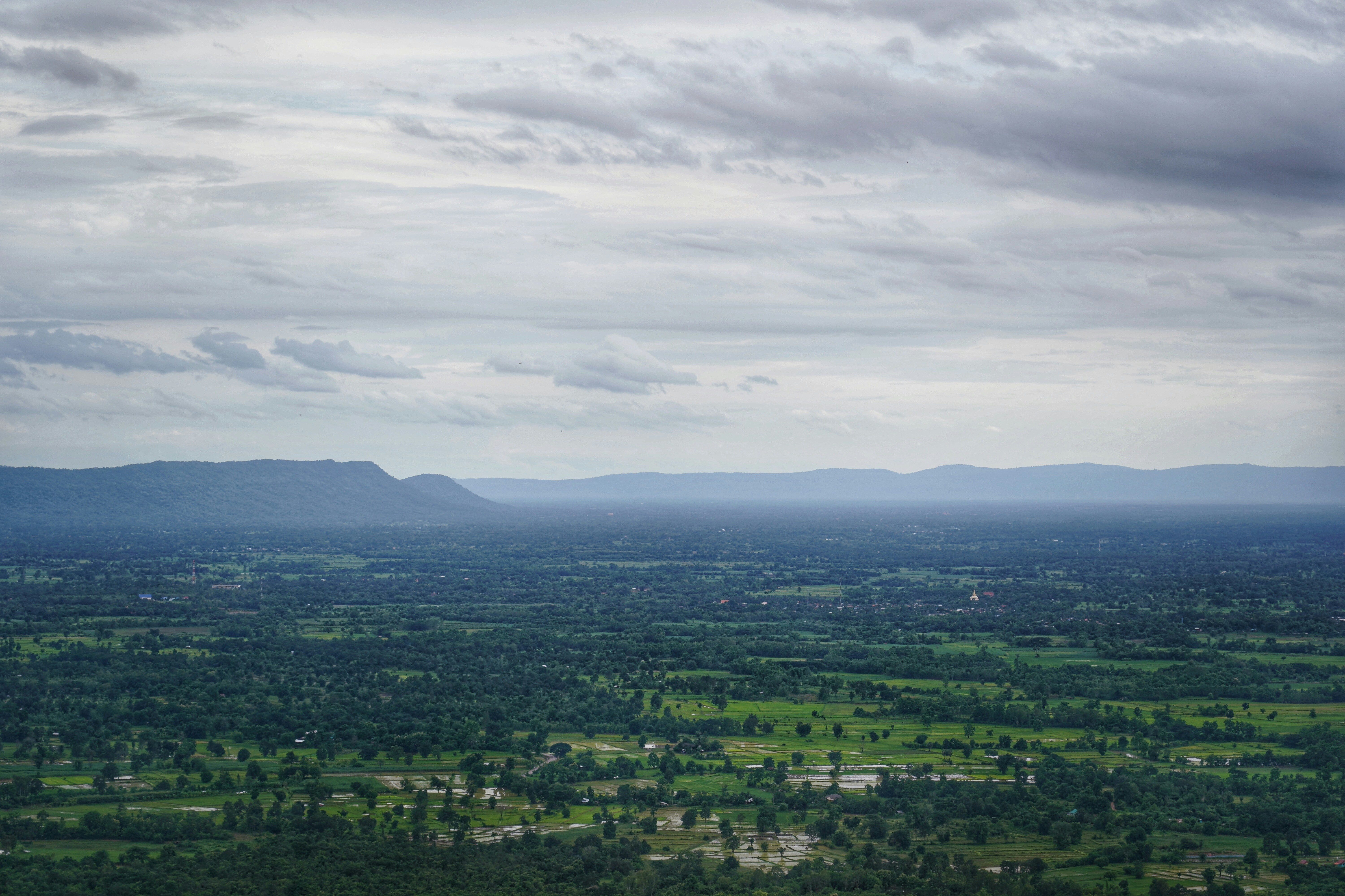 Expansive green landscape with distant mountains beneath a cloud-laden sky.