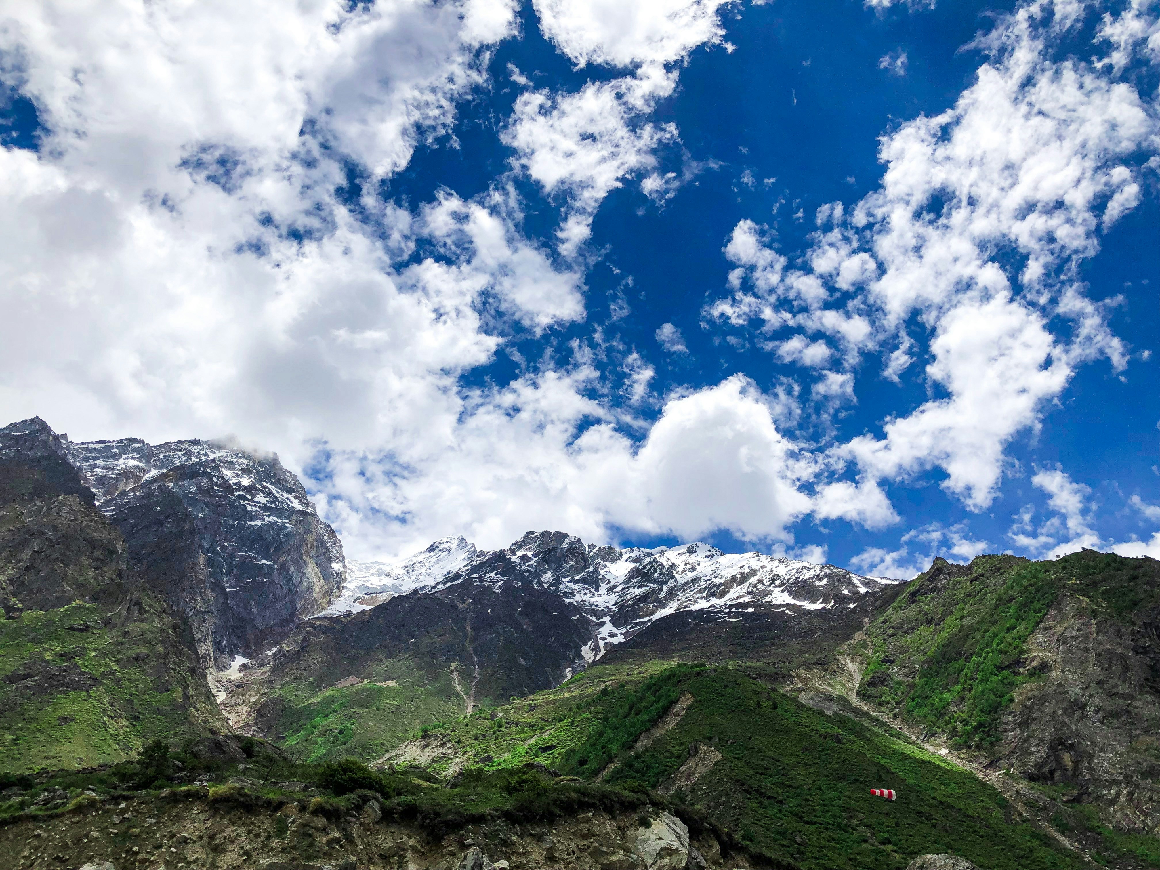 Snow-capped mountains with verdant slopes beneath a vibrant blue sky scattered with fluffy white clouds.
