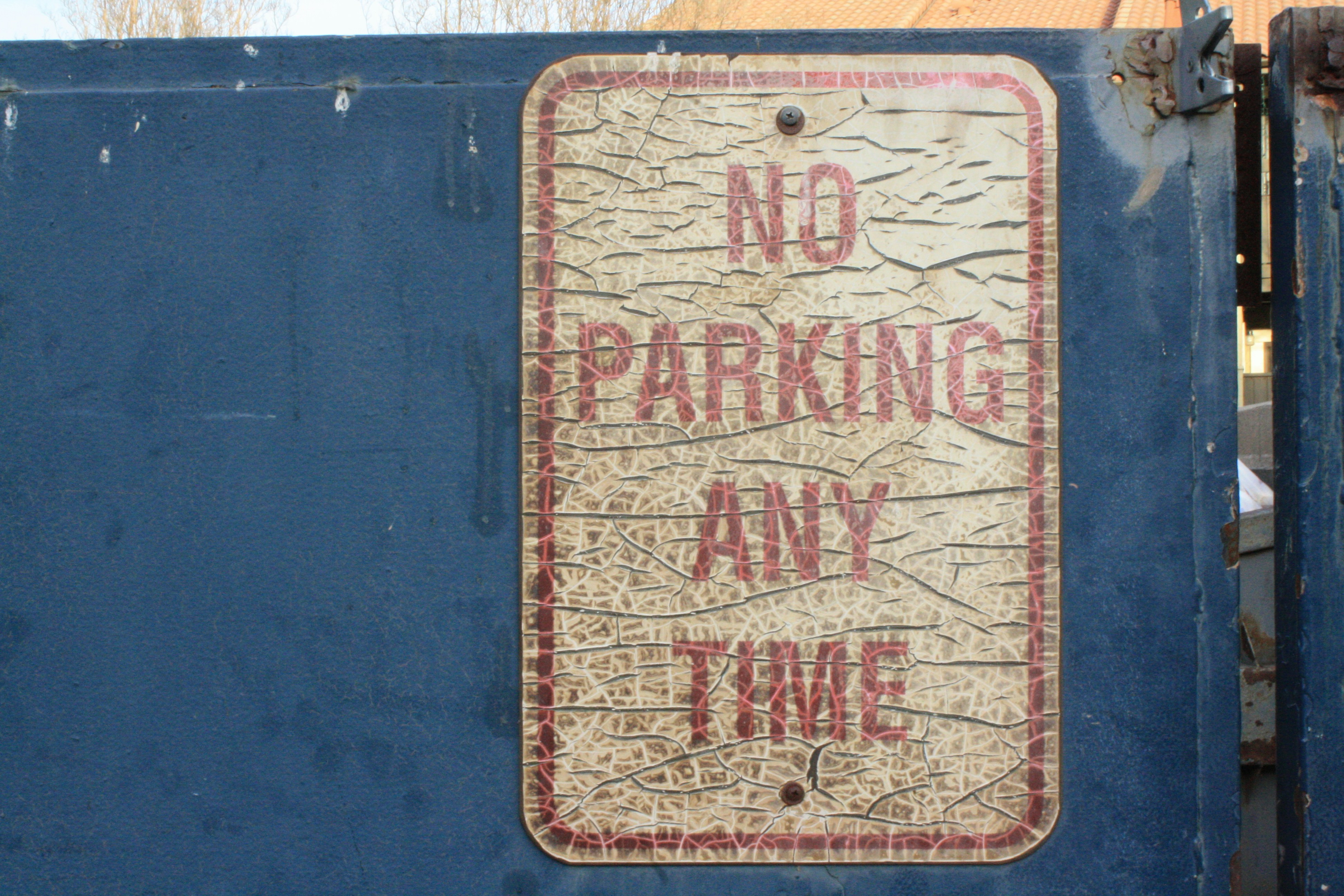 Weathered 'No Parking Any Time' sign affixed to a blue metal surface, showcasing signs of age and neglect.