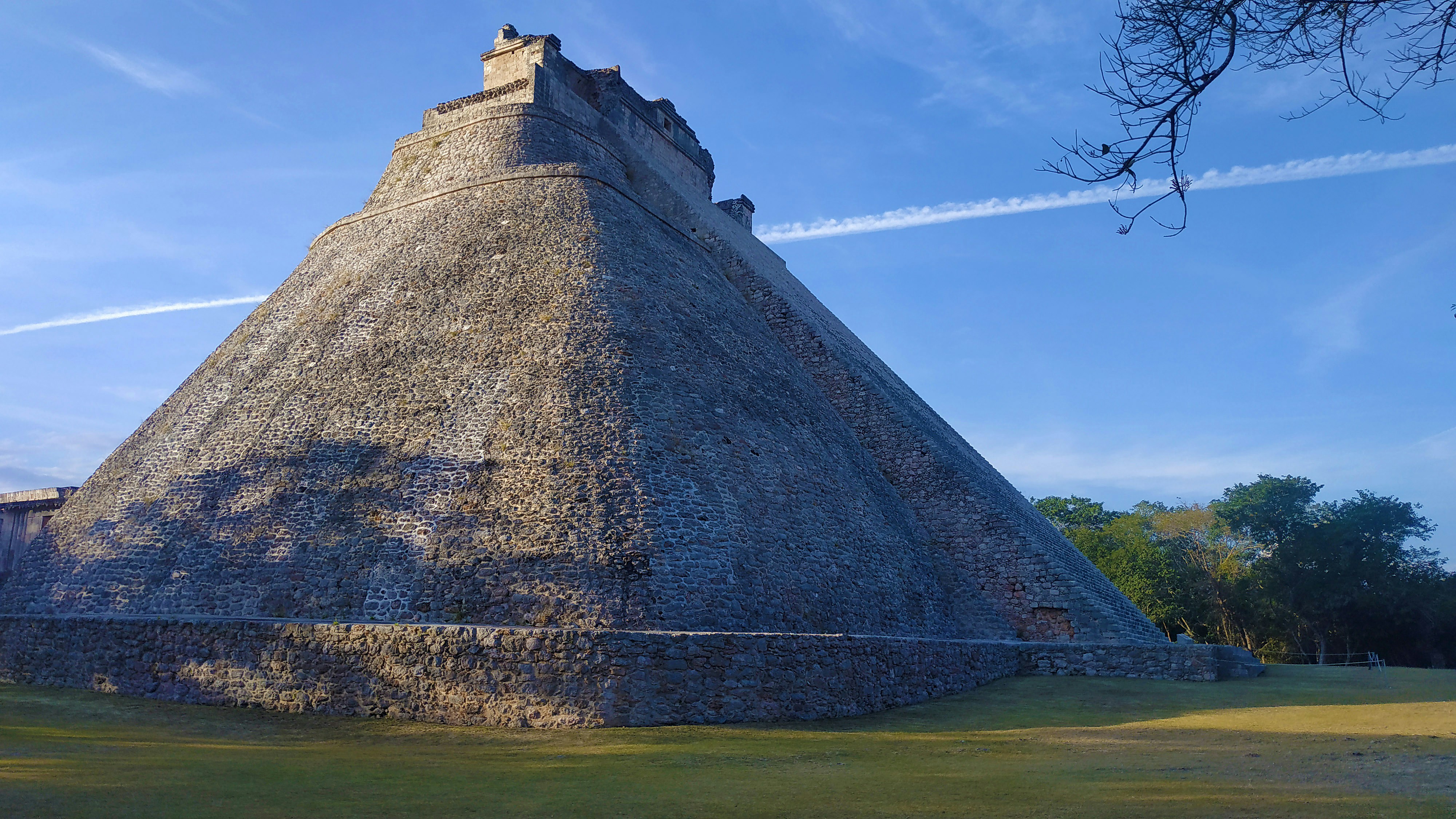 Majestic stone pyramid under a clear blue sky with a contrail overhead.
