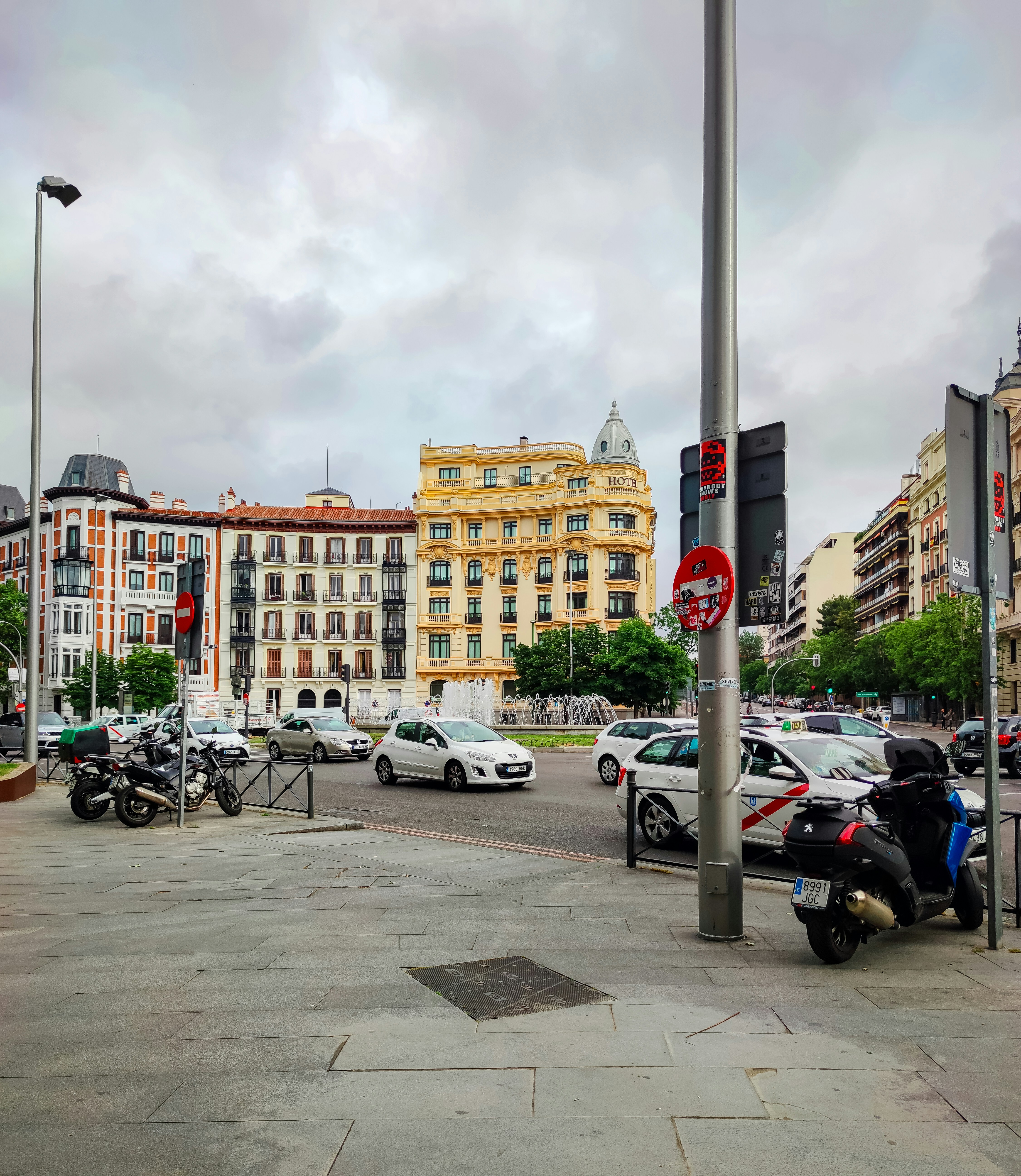 A bustling city scene showcasing elegant buildings and parked vehicles, with a hint of greenery amidst urban life.