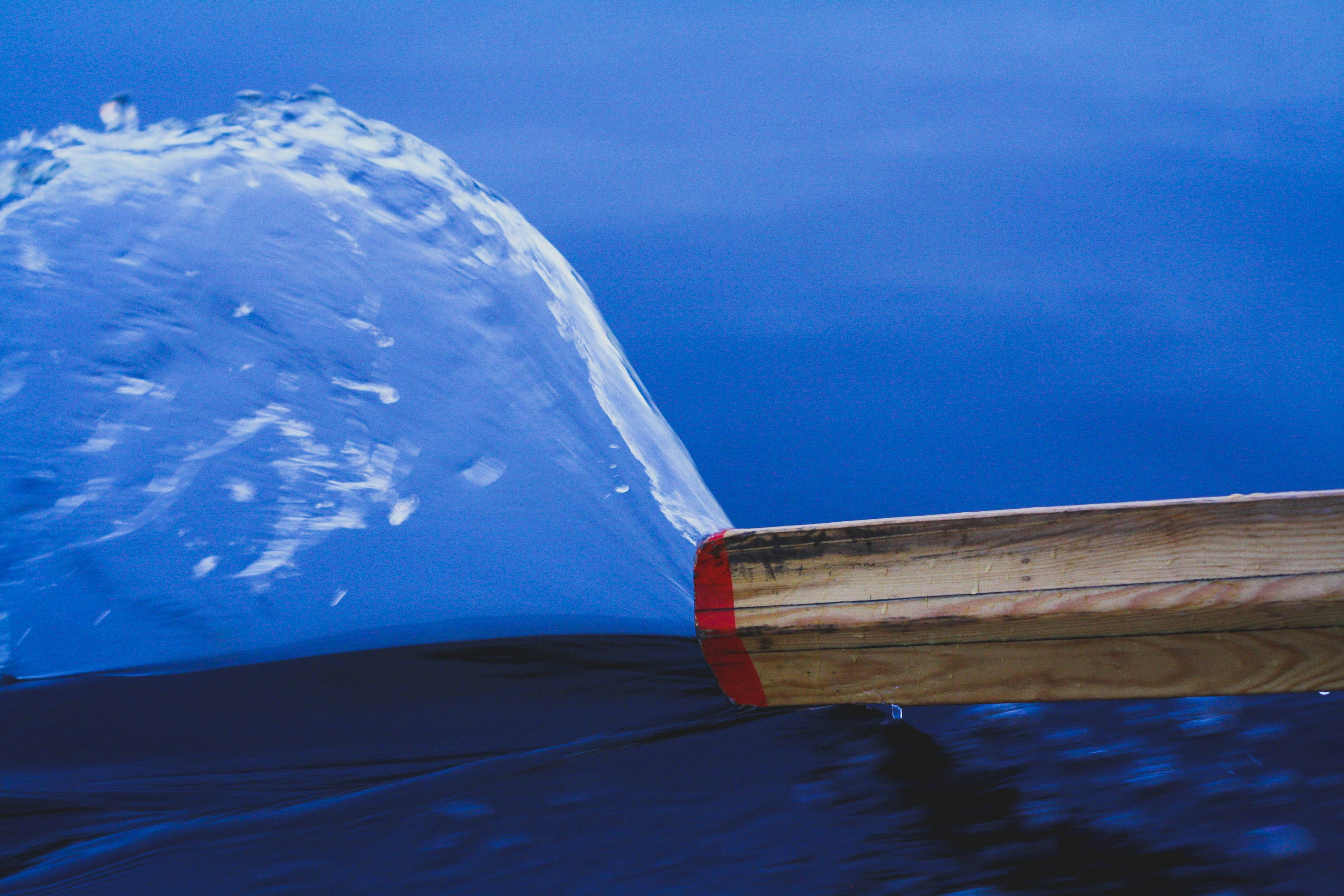 Wooden oar slicing through water, creating dynamic splashes against a serene blue backdrop.