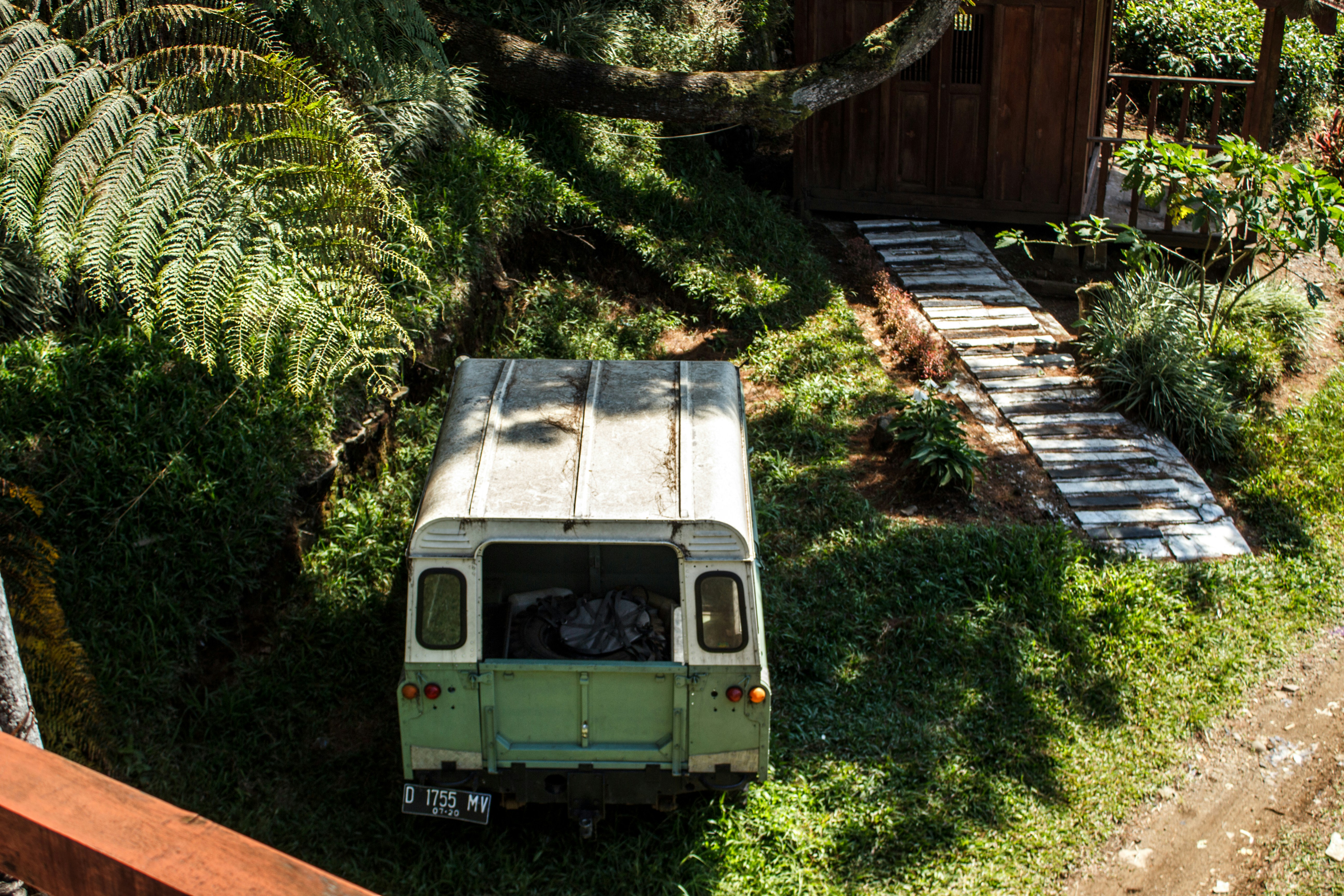 Fern-Lined Exit: A Weathered Green Van Resting by a Sunlit Timber Path
