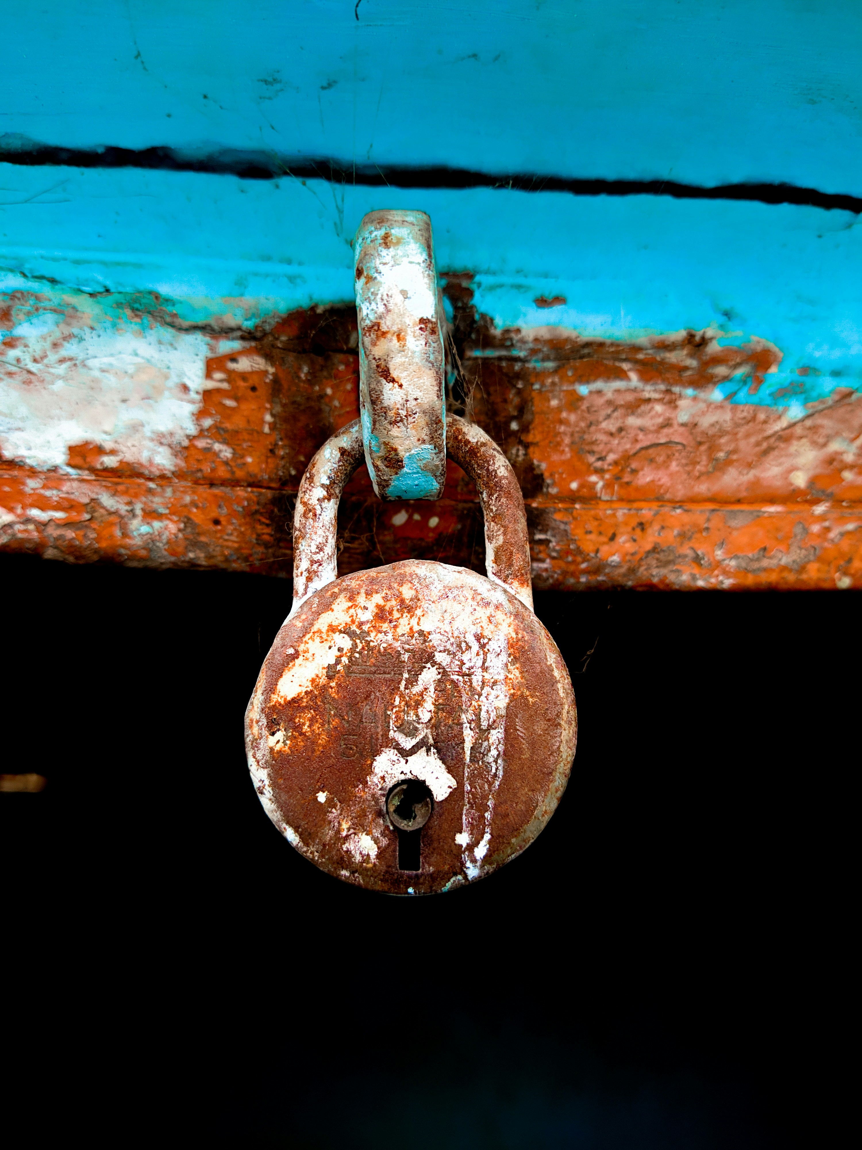 Weathered padlock hanging from a vibrant blue and orange surface, showcasing the passage of time and neglect.