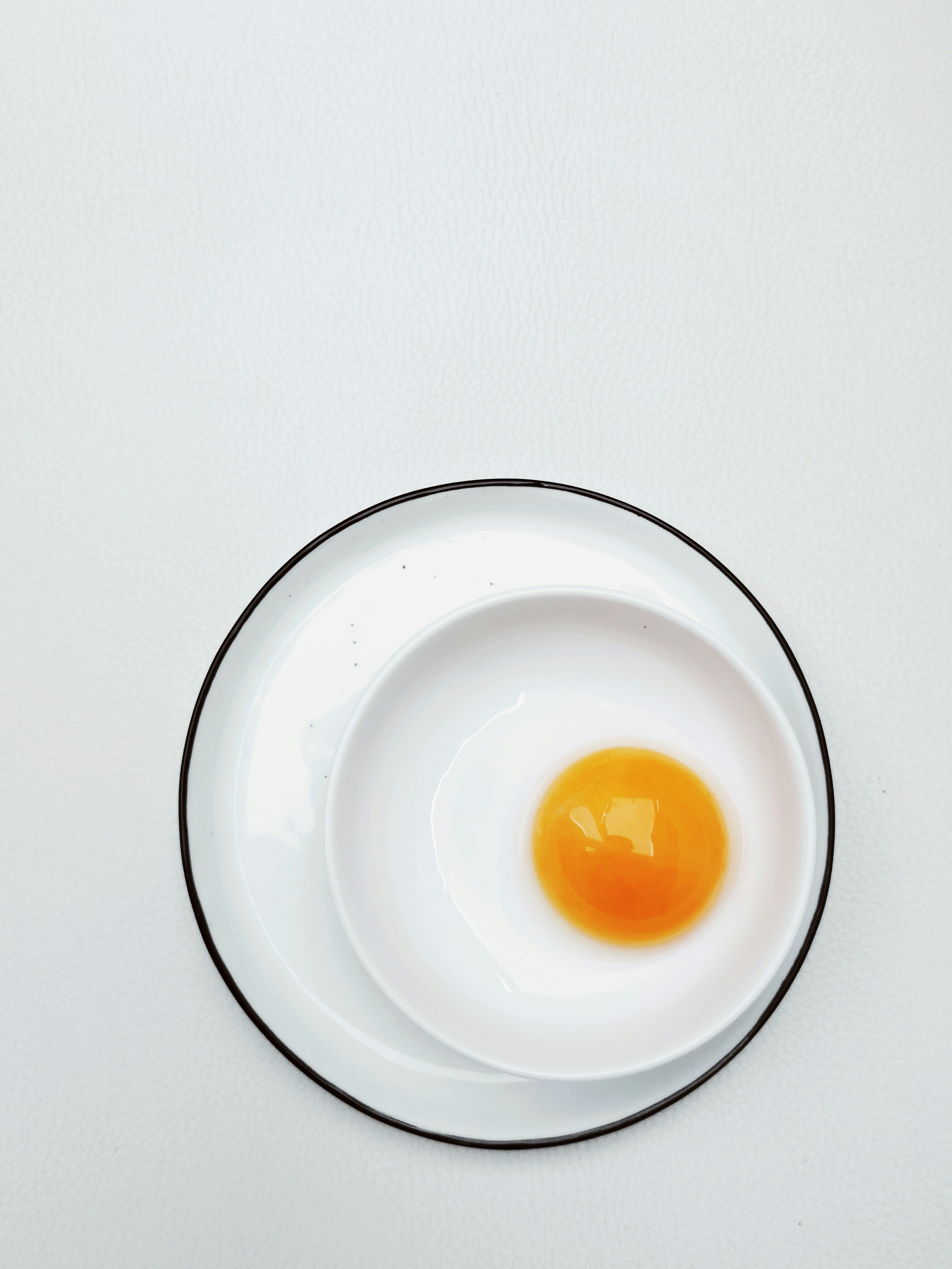 Bright yellow egg yolk resting in a small white dish atop a larger plate, showcasing a minimalist culinary presentation.