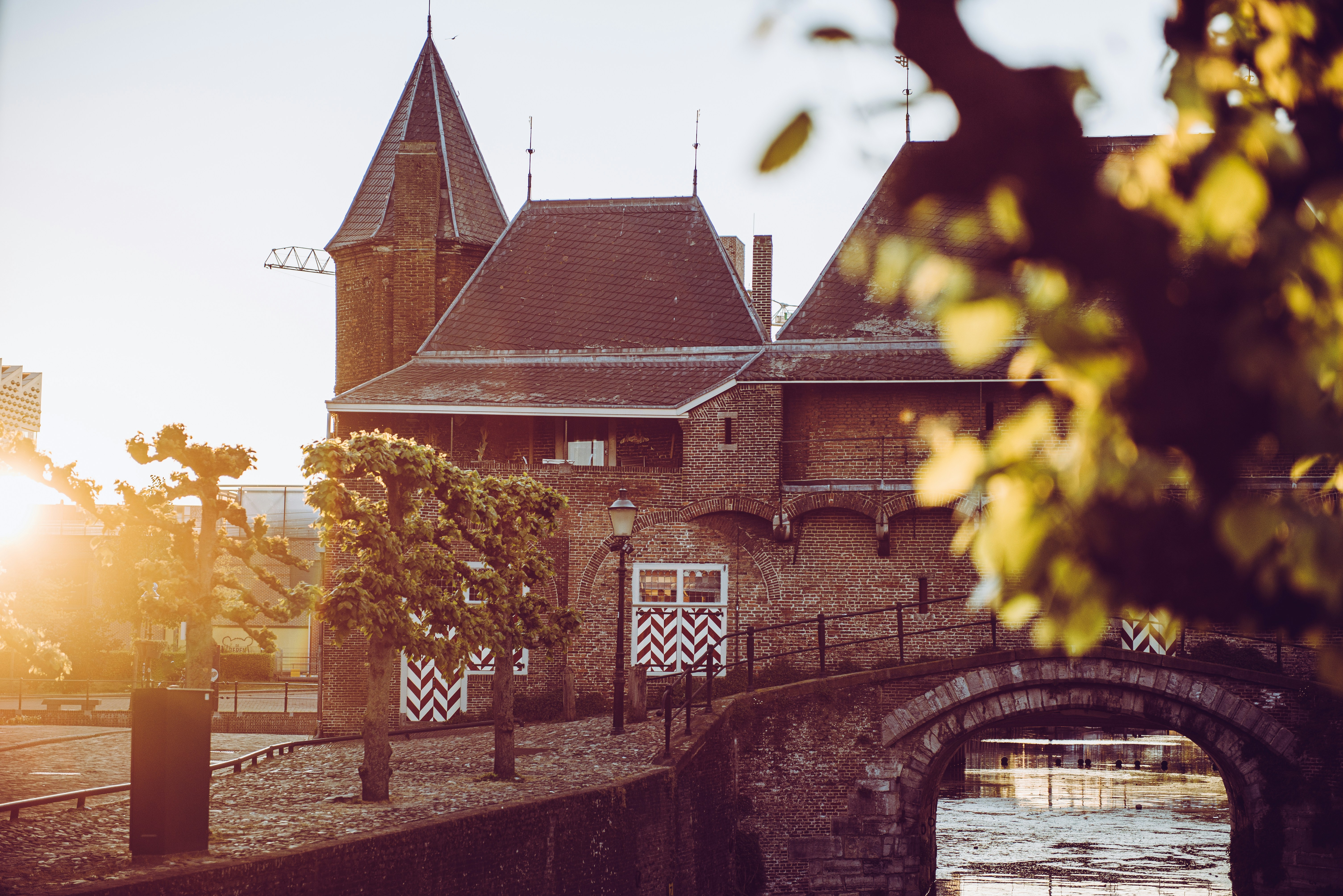 Historic brick building with turrets beside a river, illuminated by warm sunset light.