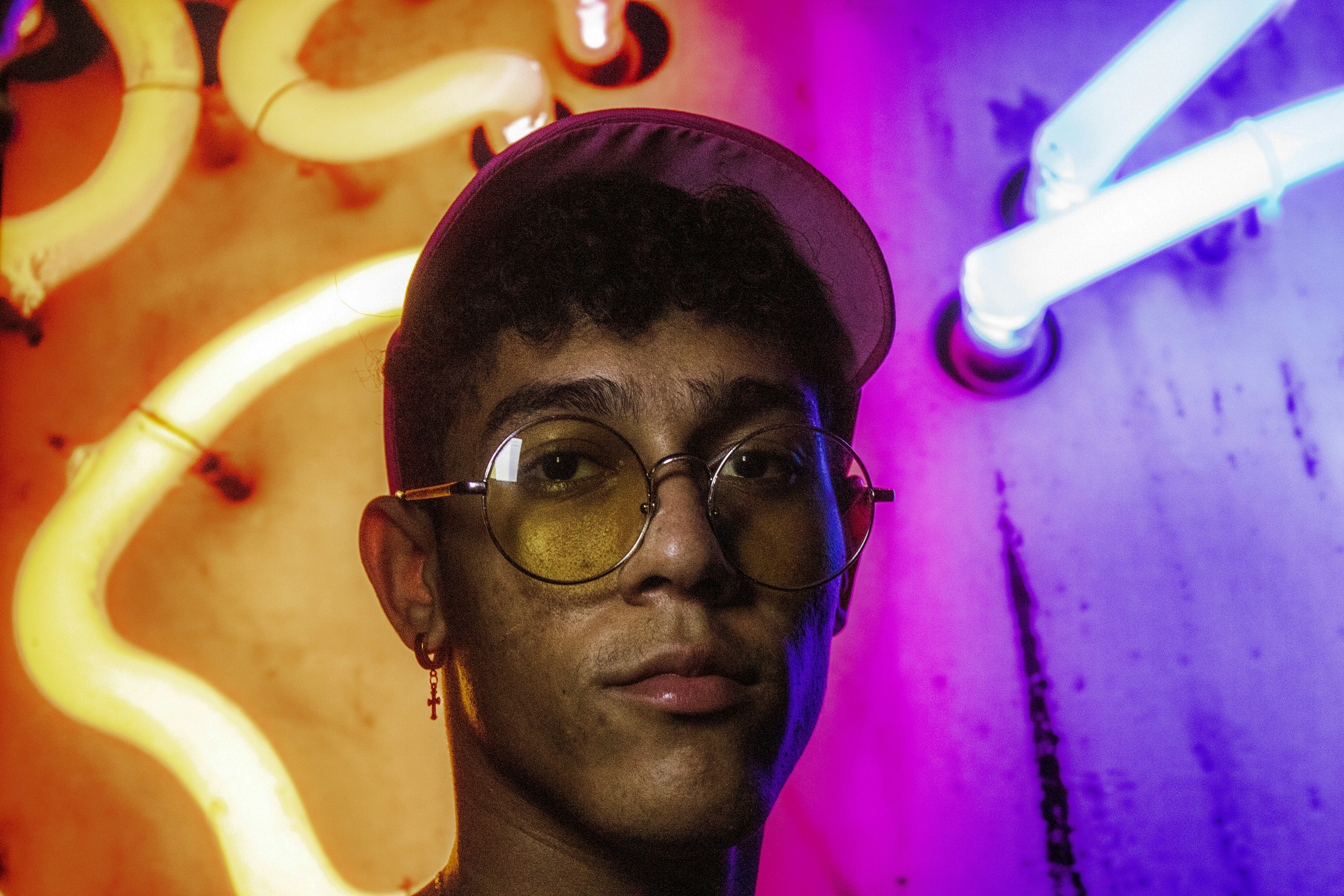 Person with yellow-tinted glasses against a colorful neon backdrop.