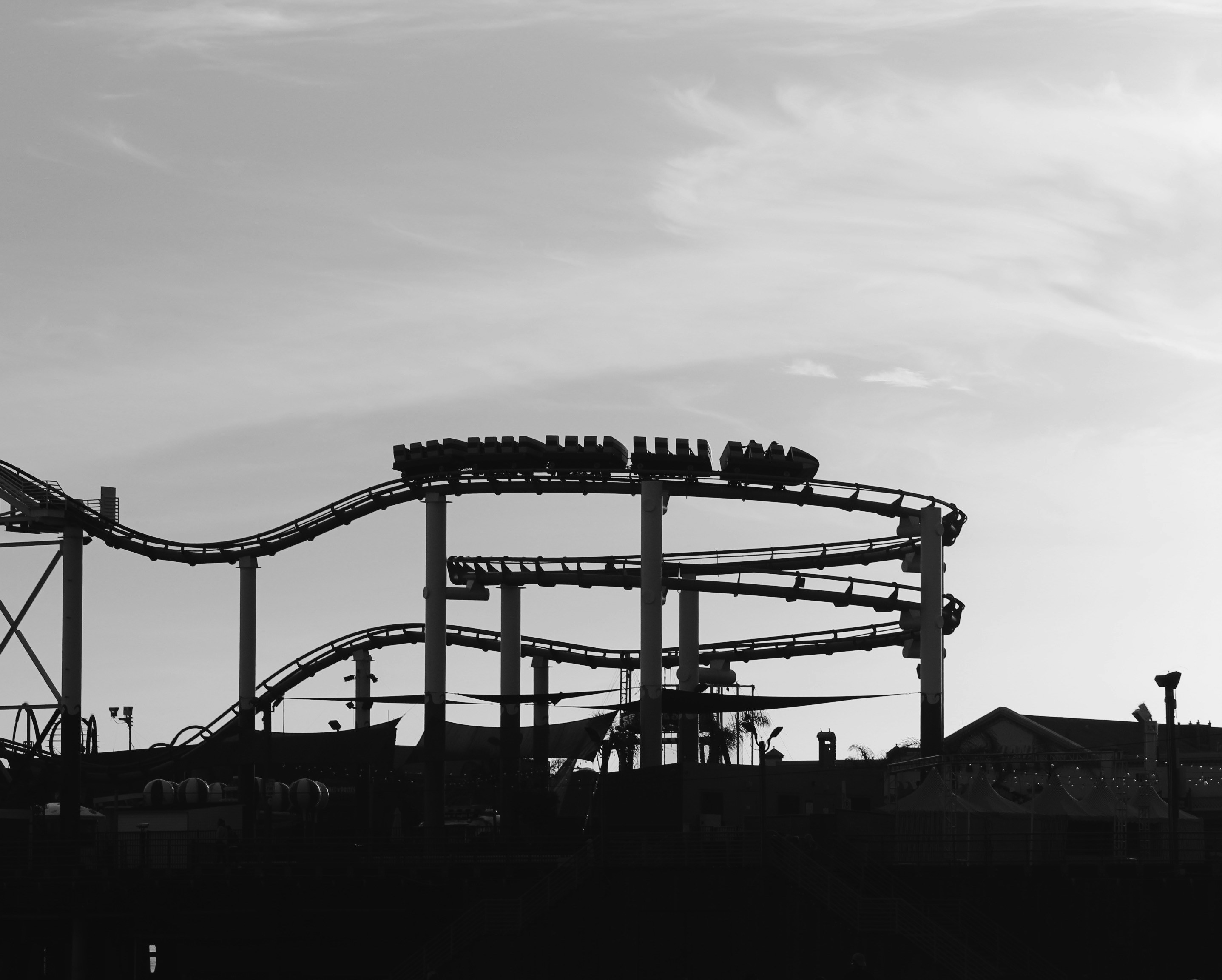 Silhouetted roller coaster tracks intertwine against a cloudy sky, capturing the essence of amusement and adventure.