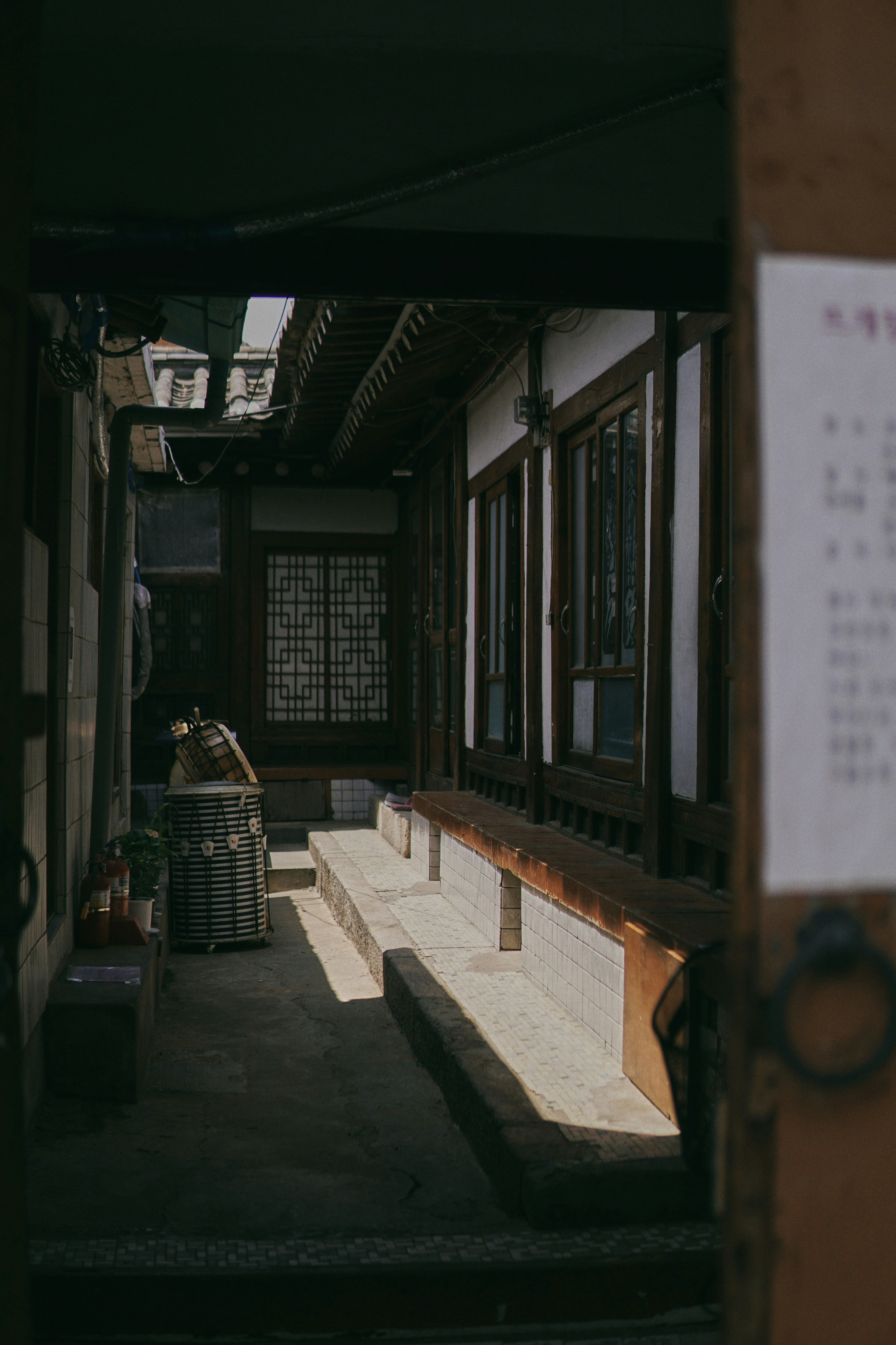 A narrow corridor of a traditional Korean hanok, showcasing wooden architecture and stone steps illuminated by soft sunlight.