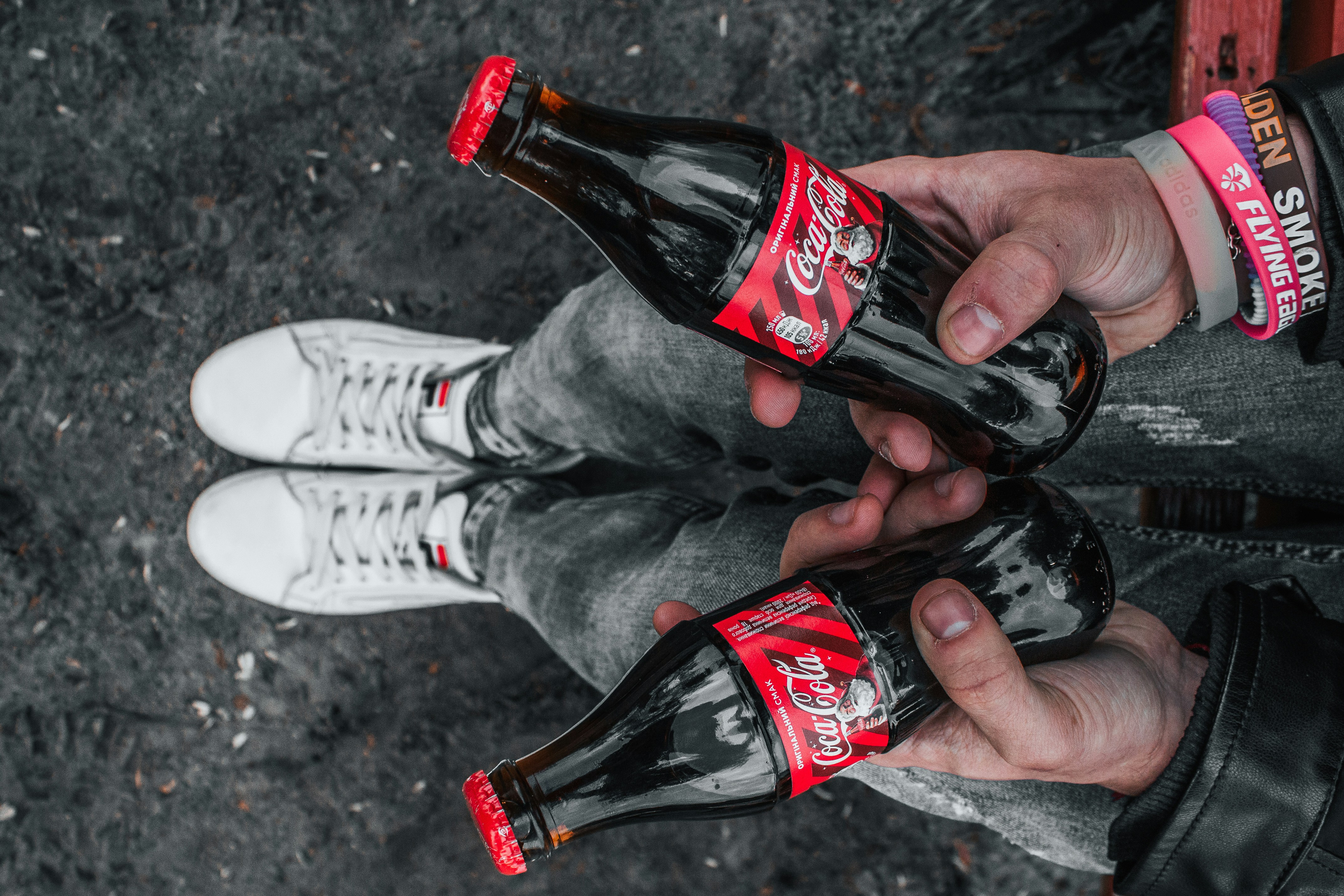Overhead Toast: Two Coca-Cola Bottles Cradled Over White Sneakers
