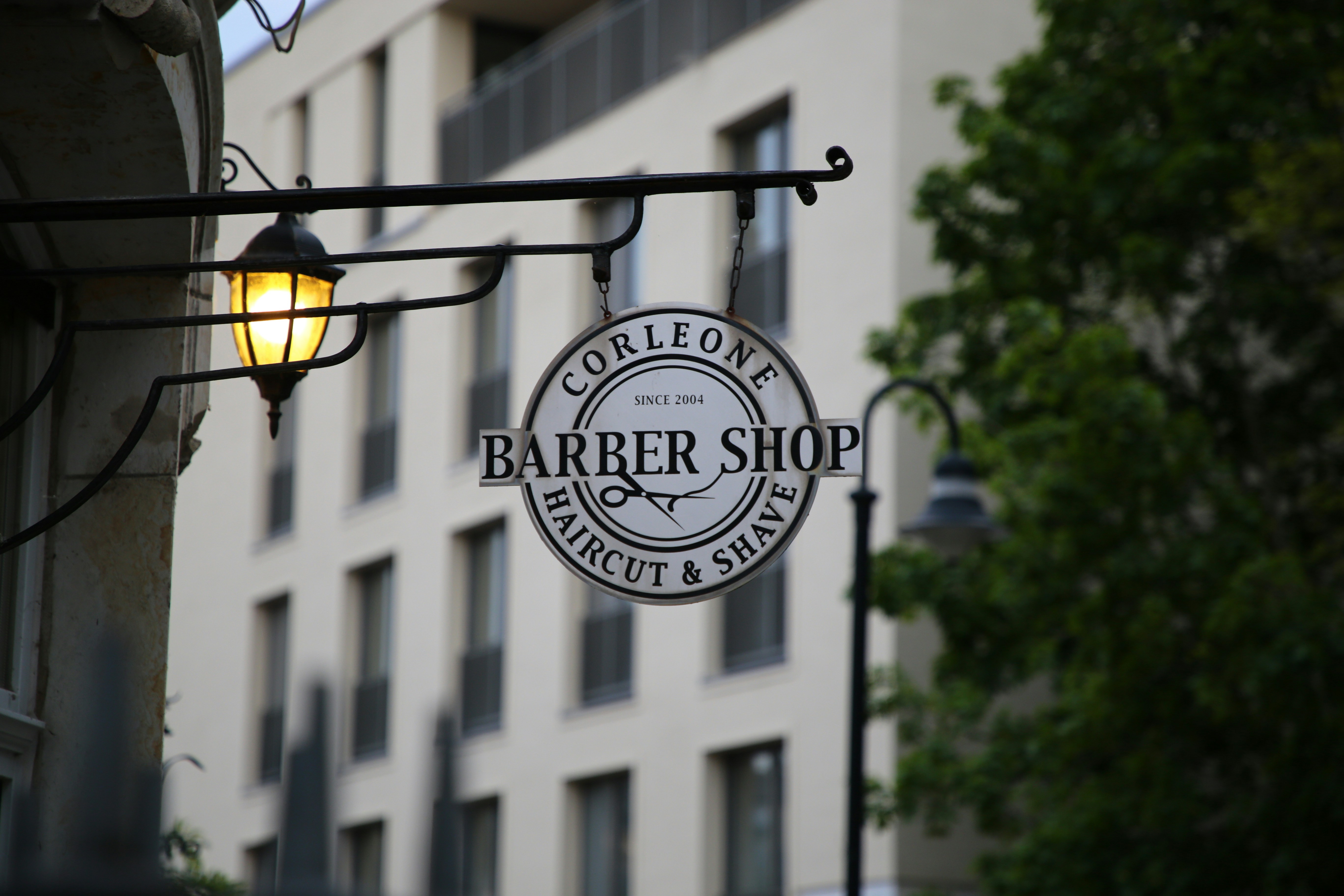 Vintage barber shop sign hanging against a modern urban backdrop. The warm glow of the lamp adds charm to the scene.