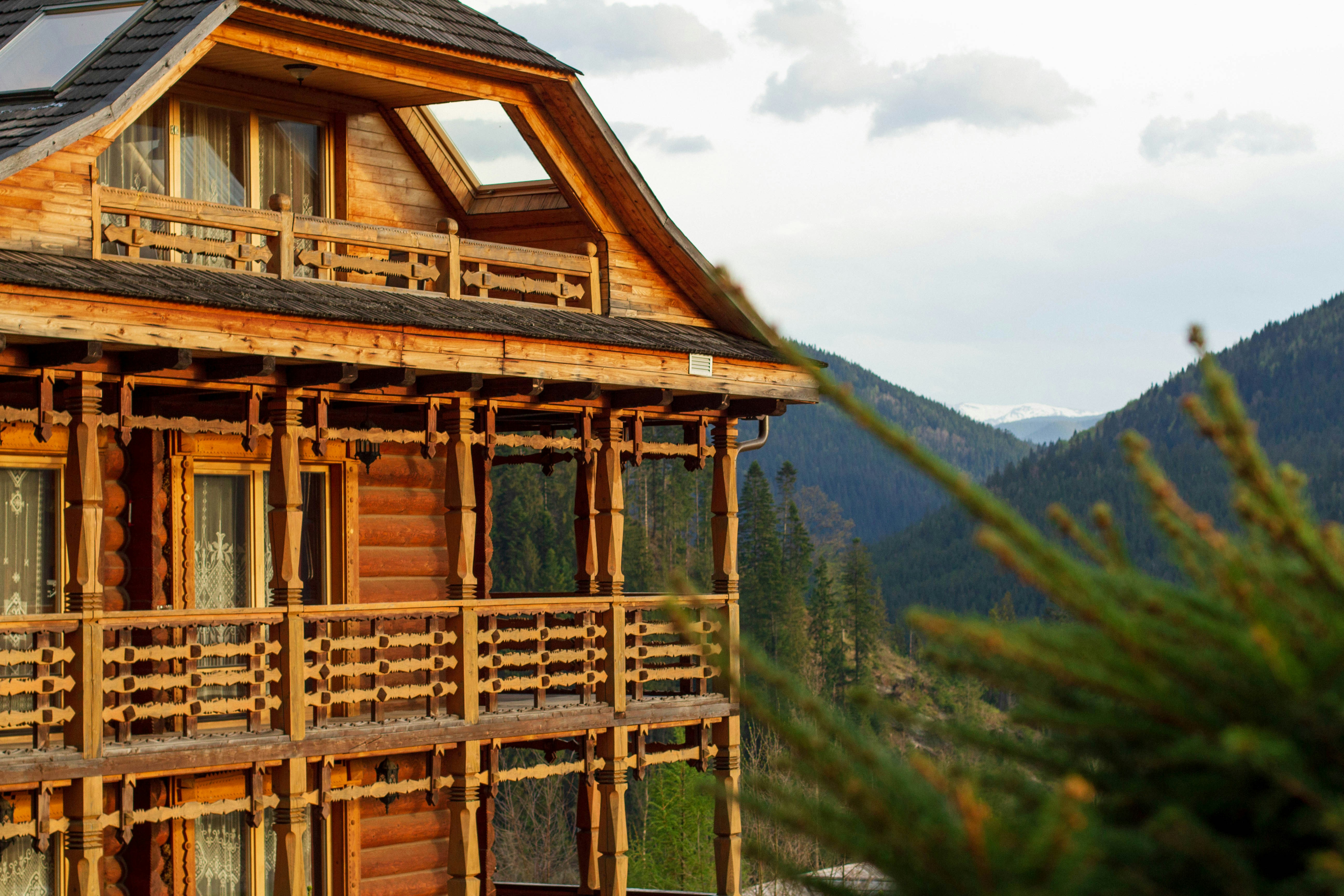 Wooden lodge with intricate balcony details set against a backdrop of rolling hills and distant peaks.