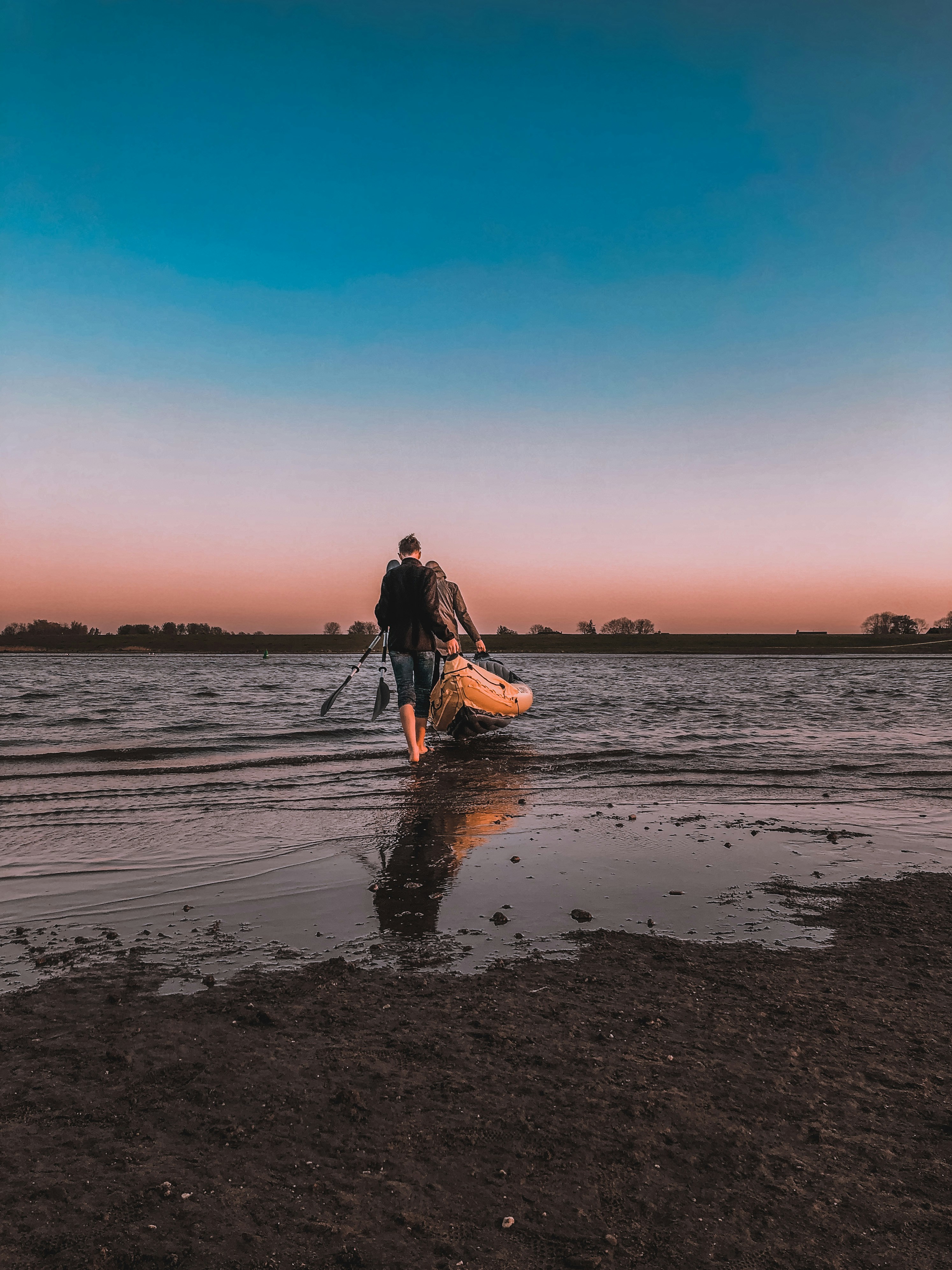 Twilight Crossing: Two Adventurers Haul a Dinghy into a Calm Sunset
